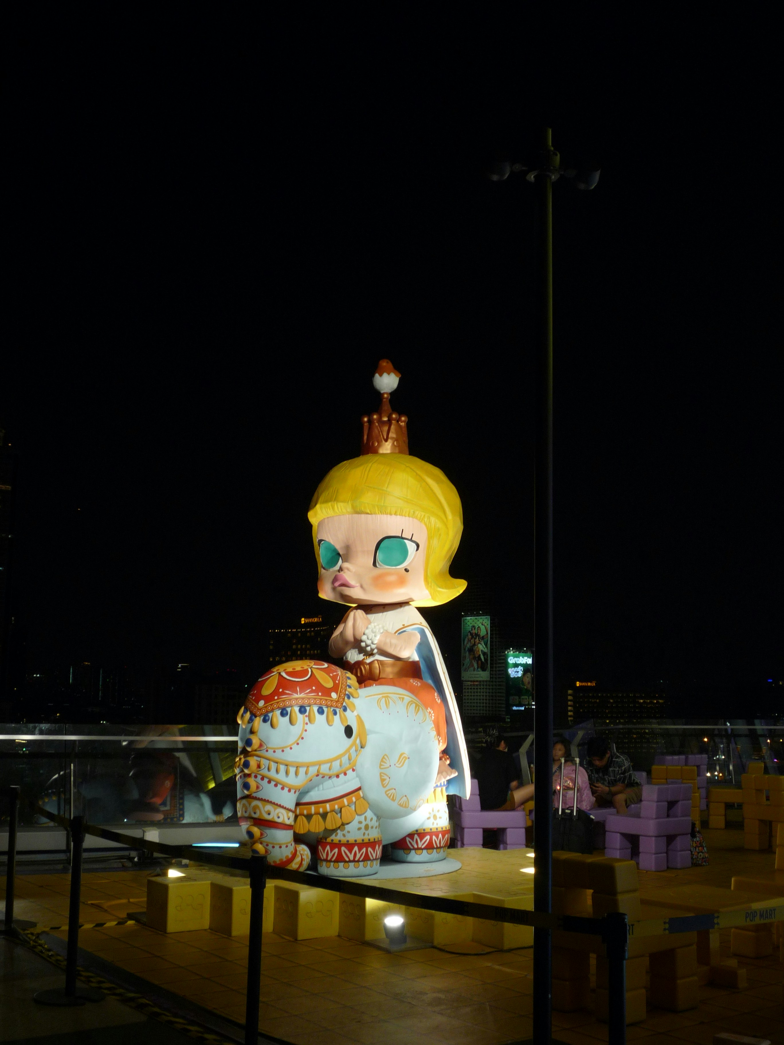 Nighttime Neon Figure: A Gigantic Cartoon Character Guards a Playful Scene