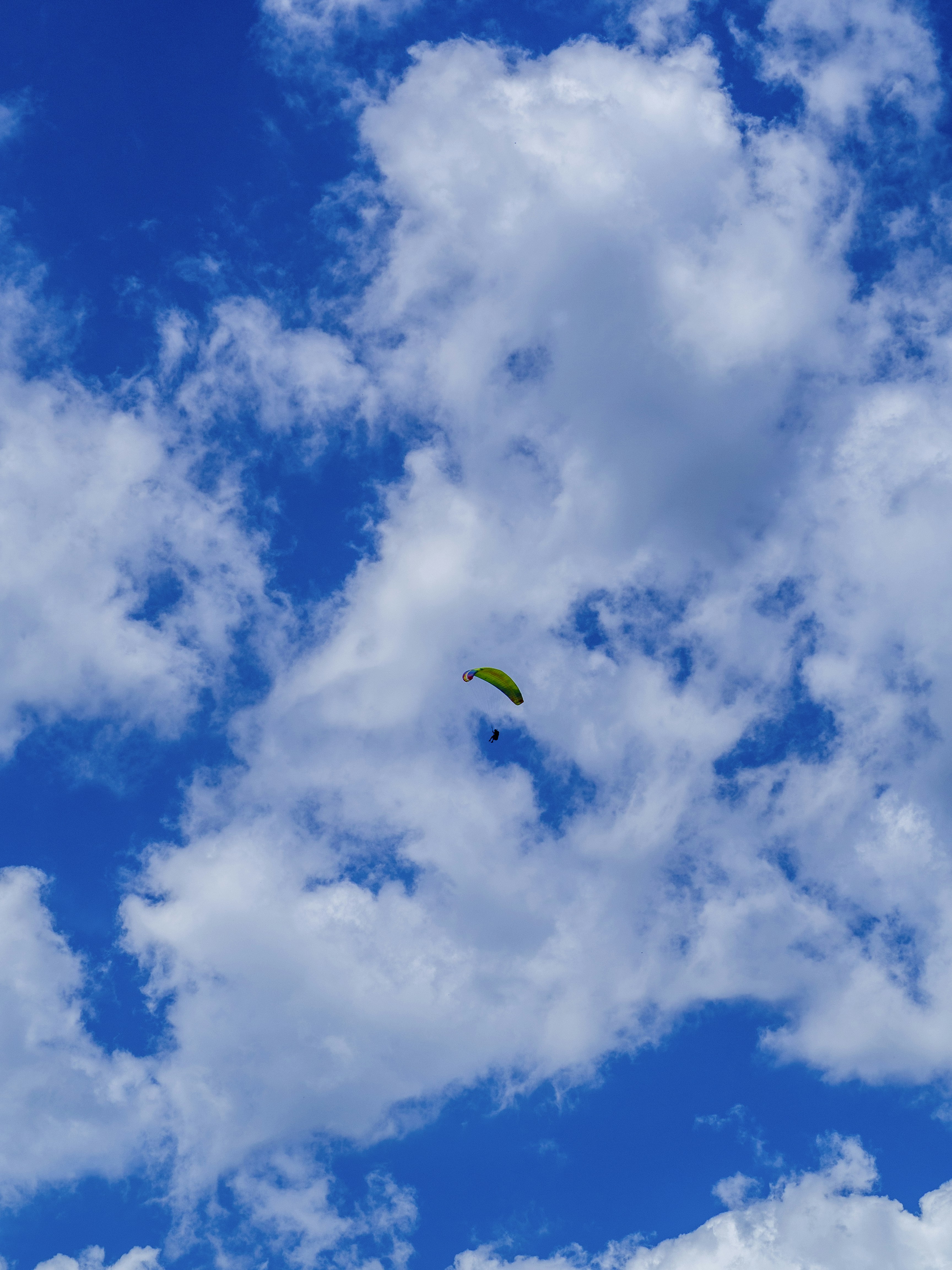 Green paraglider traces a bright arc through a scattered-cloud blue sky