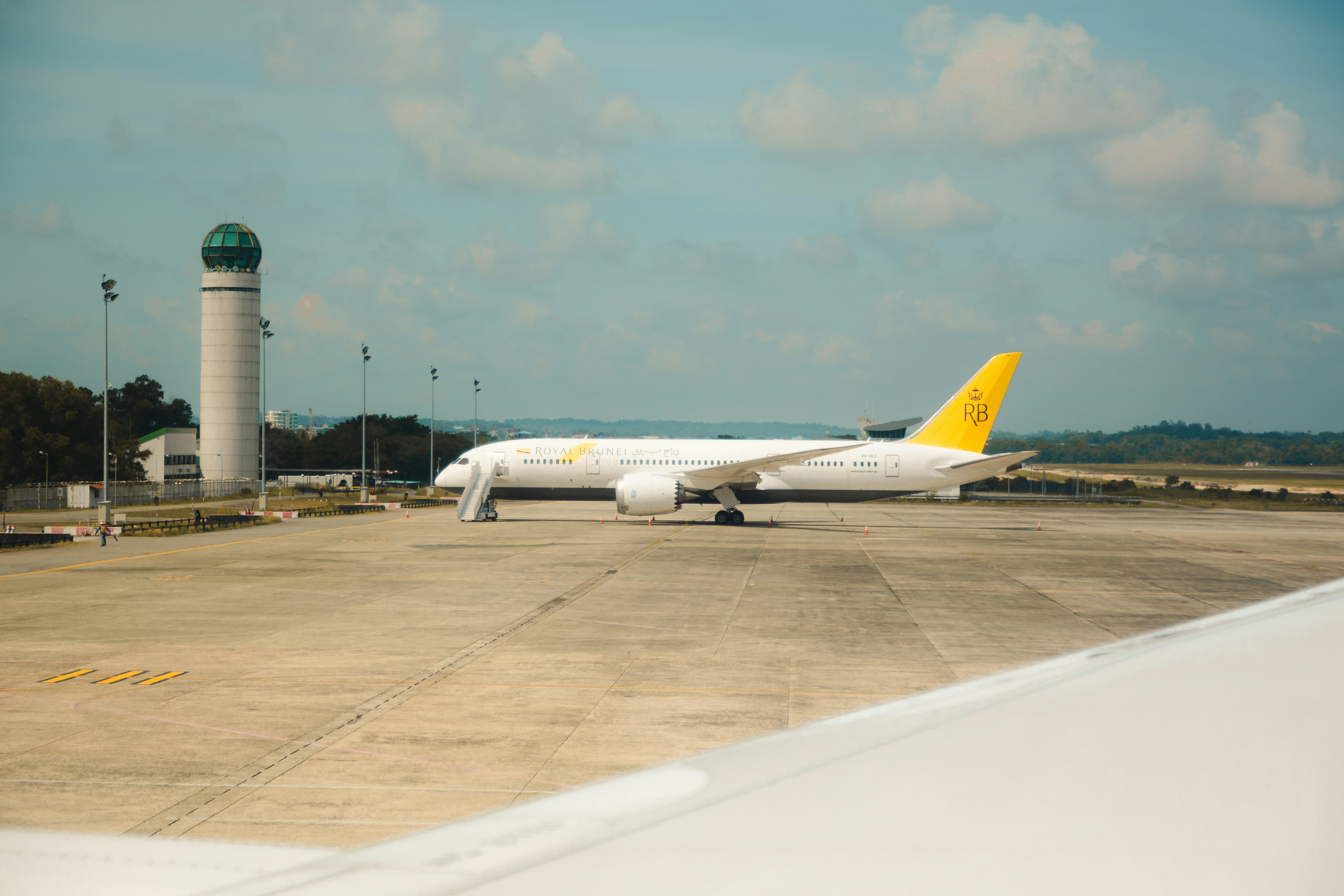 Yellow-tailed airliner on tarmac under a bright, partly cloudy sky