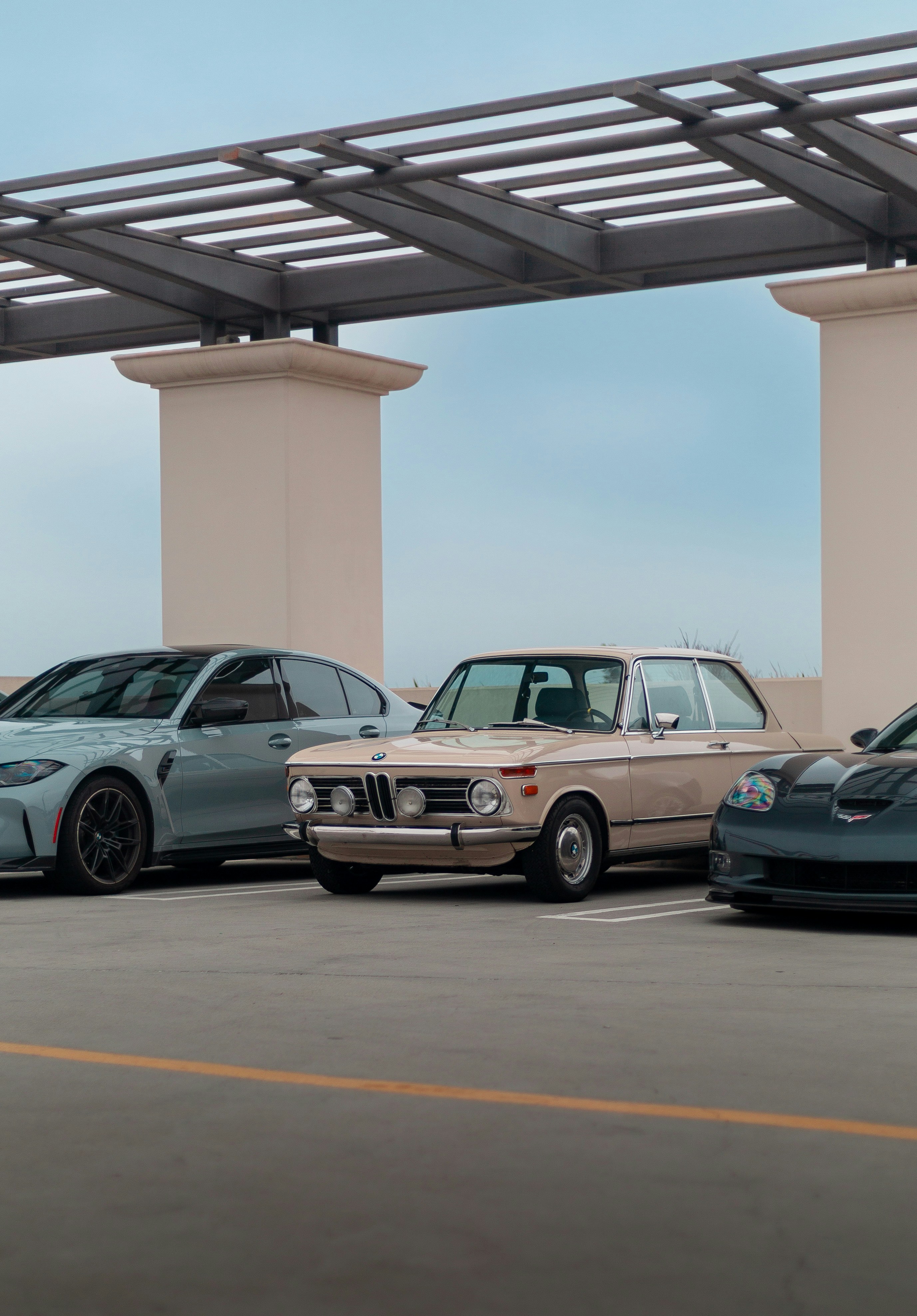 Past Meets Present: A beige vintage BMW Nestled Between Modern Muscle