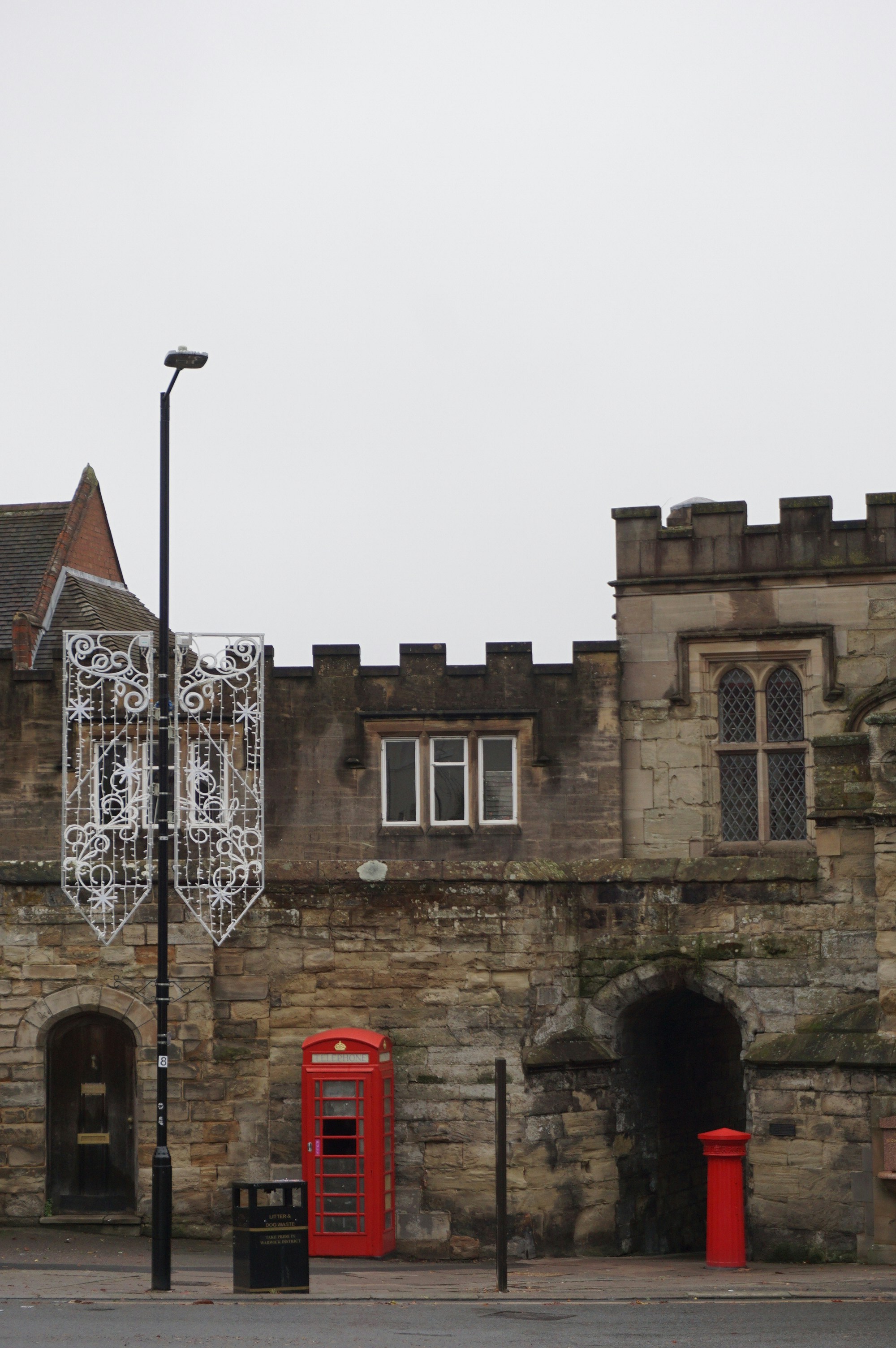 Red Mailbox and Medieval Facade Beneath Overcast Sky