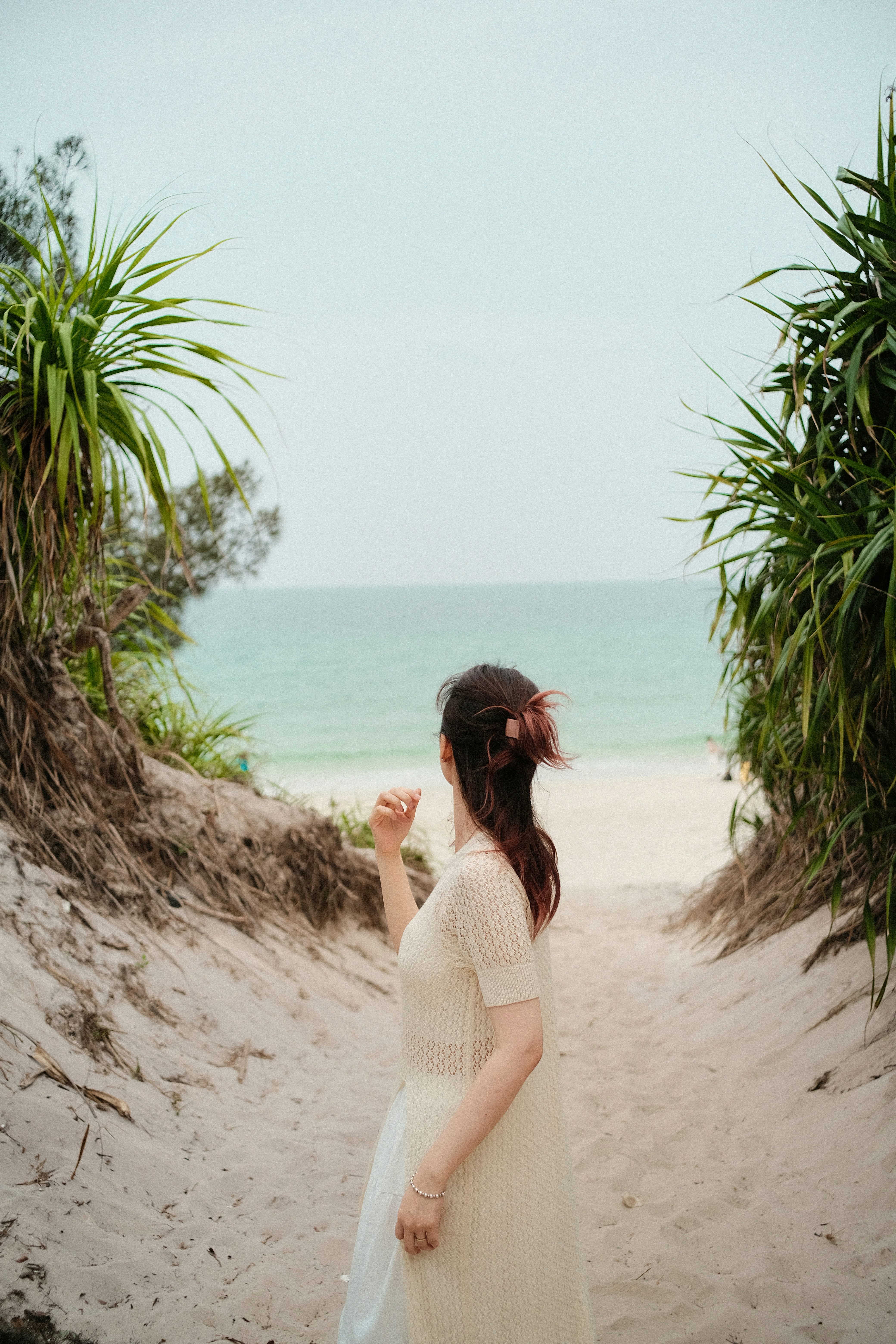 Sand Path to Serenity: A Woman in Cream Steps Toward the Ocean