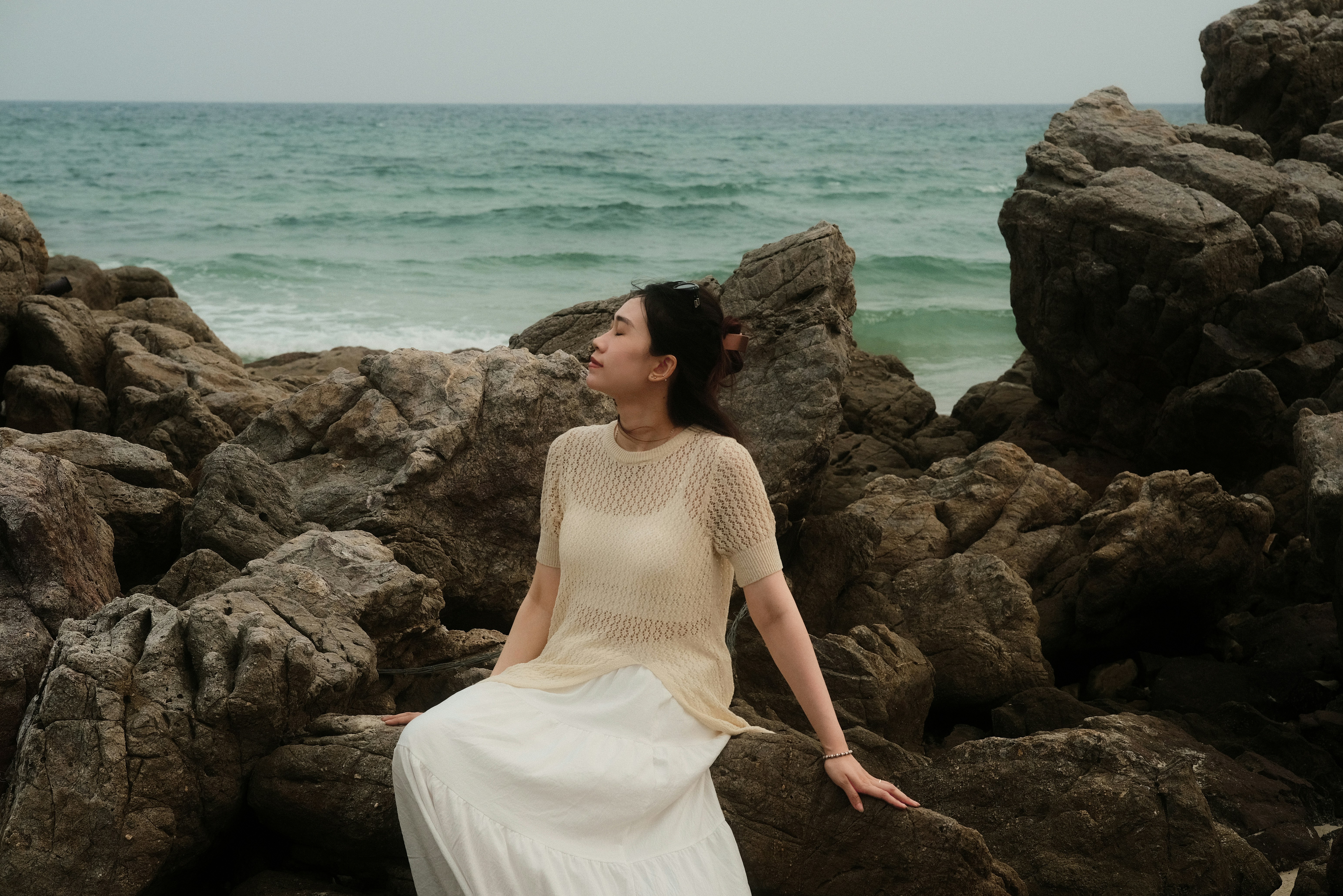 Seaside Solace: Woman in cream knit on weathered rocks
