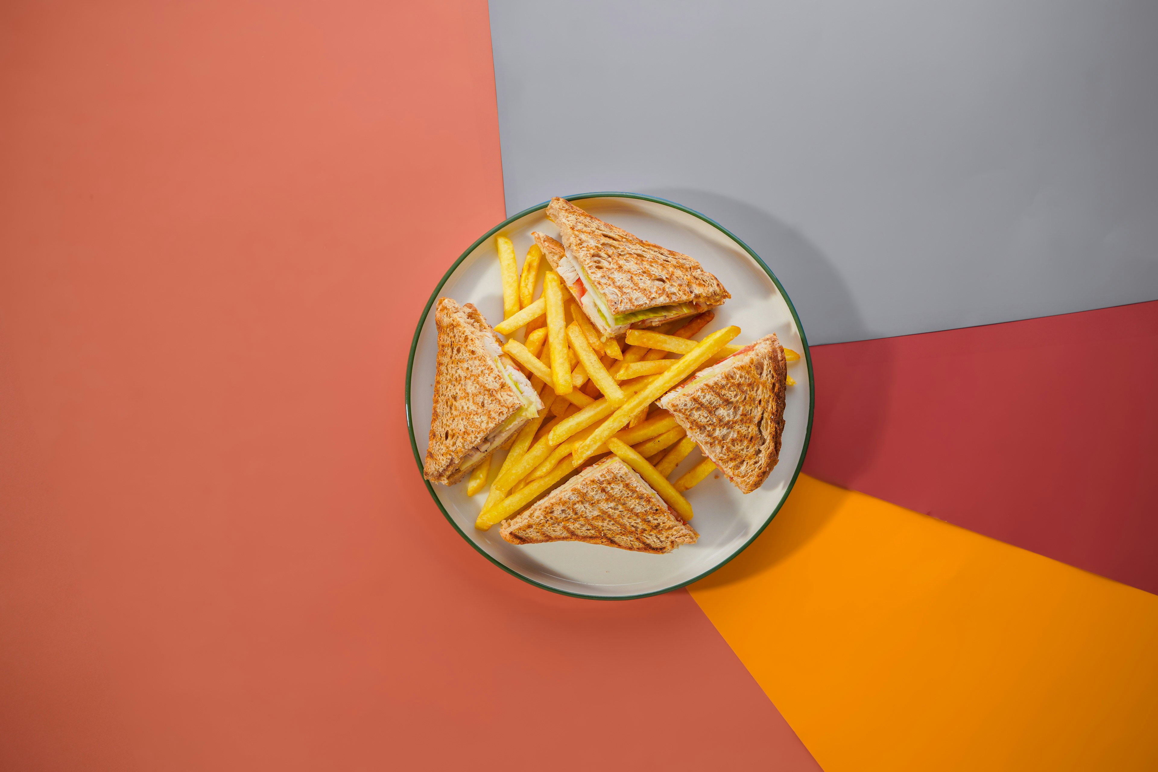 Plate of triangle-sliced grilled sandwiches with fries against a geometric colored backdrop