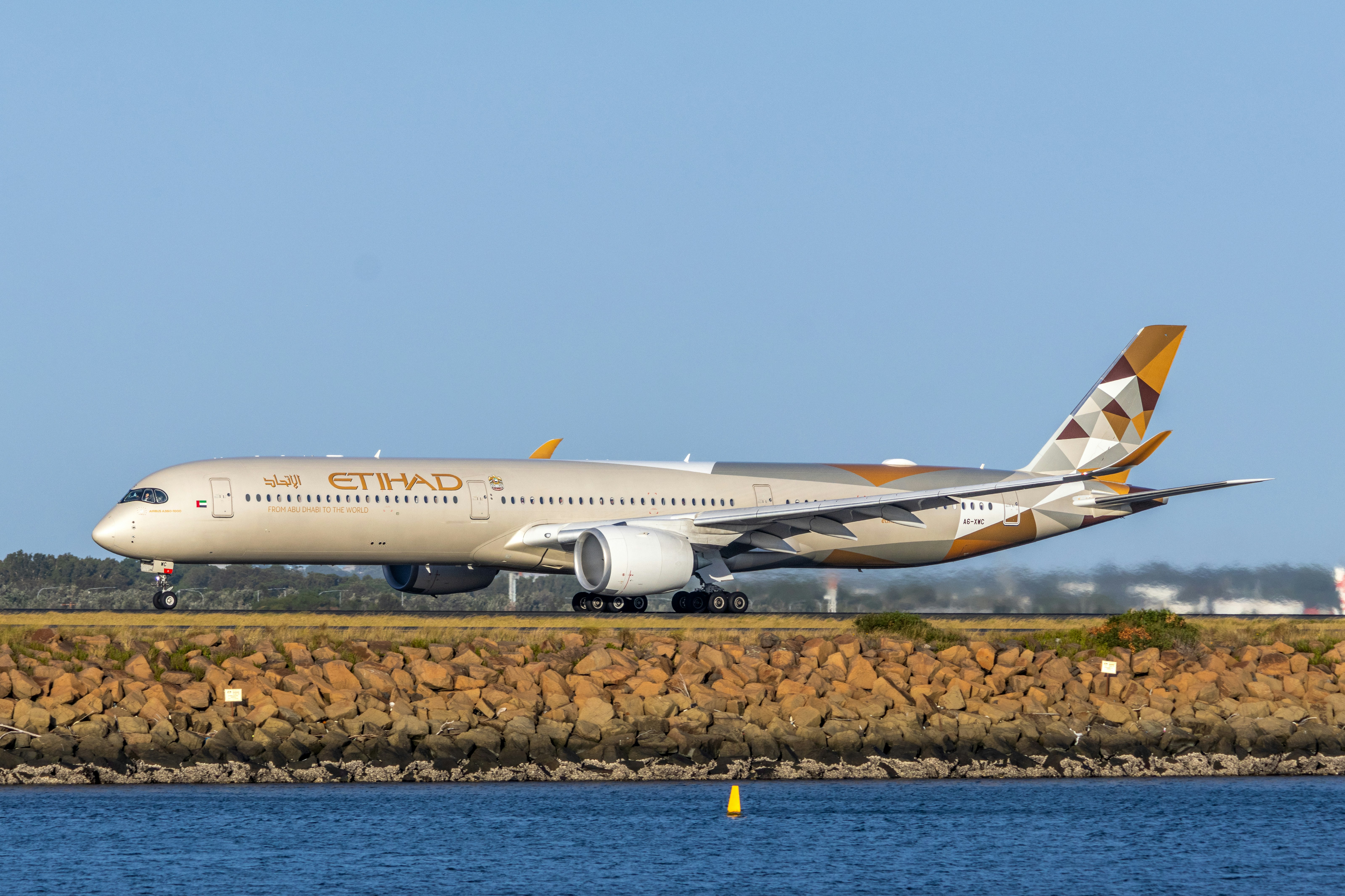 Etihad Dreamliner gliding past a stone breakwater at quay side