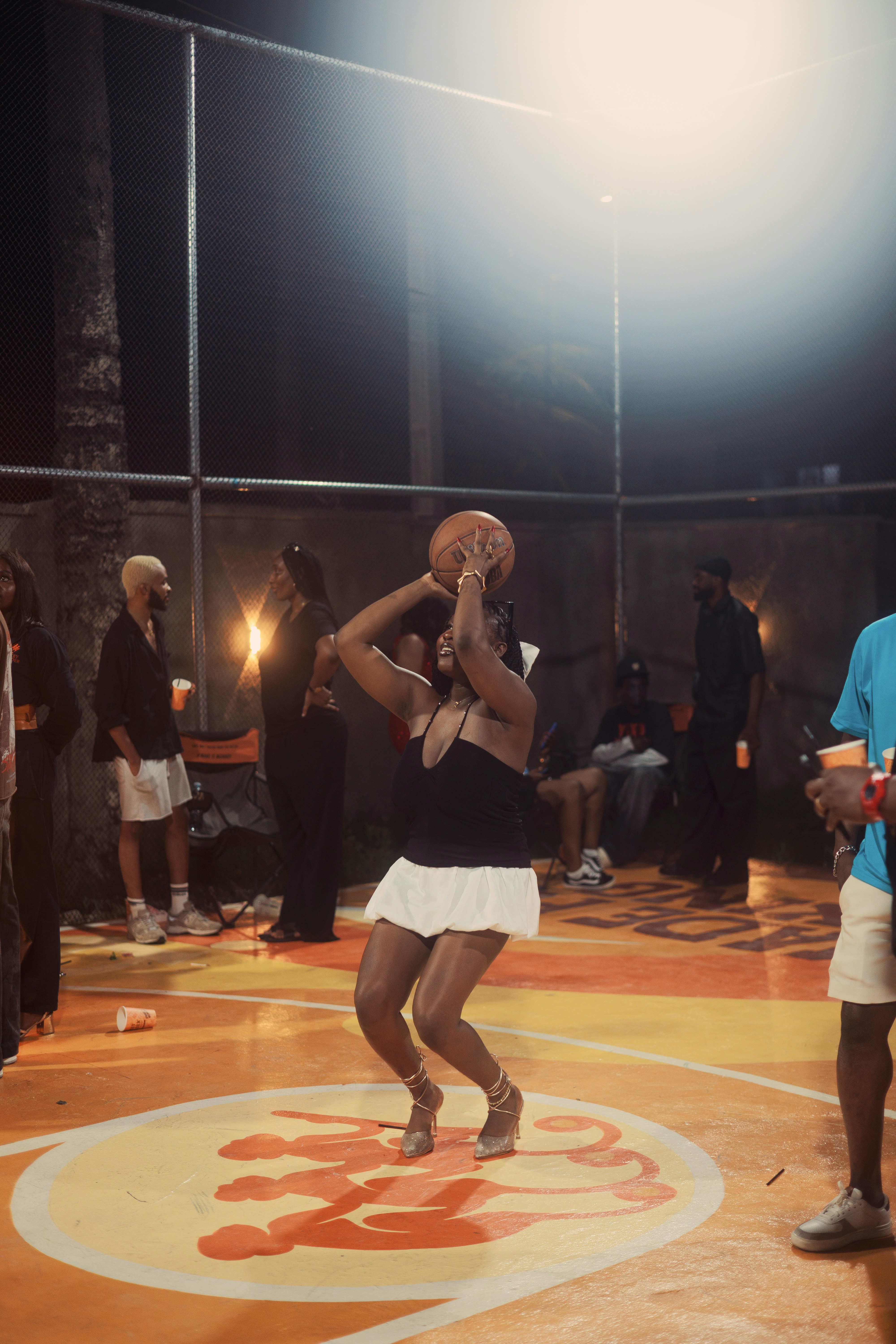 Crouched dancer with hat in a dimly lit outdoor court during a social gathering