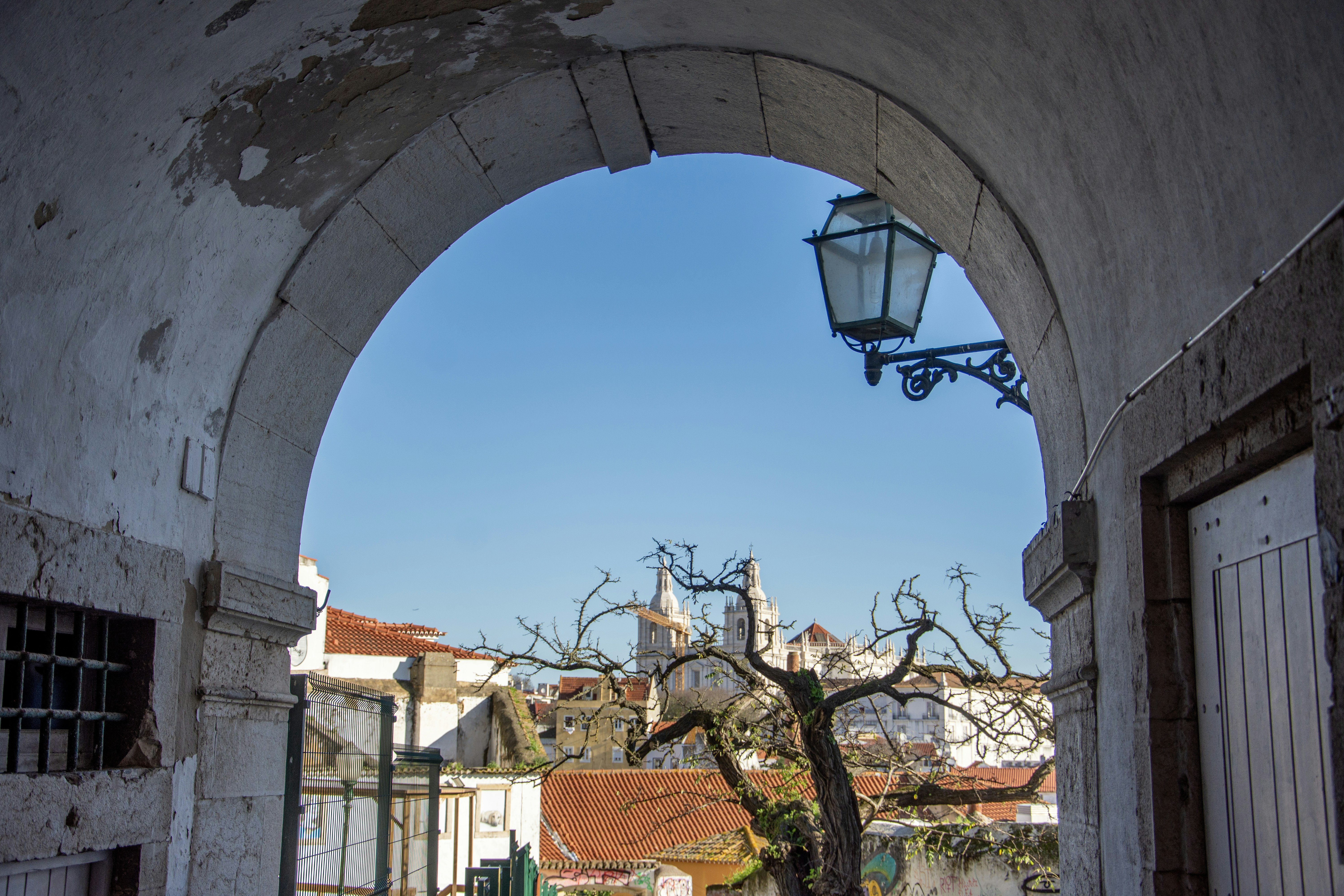 Arched View to a Sunlit Town: A Quiet Portal Framing a Lantern and Distant Steeples