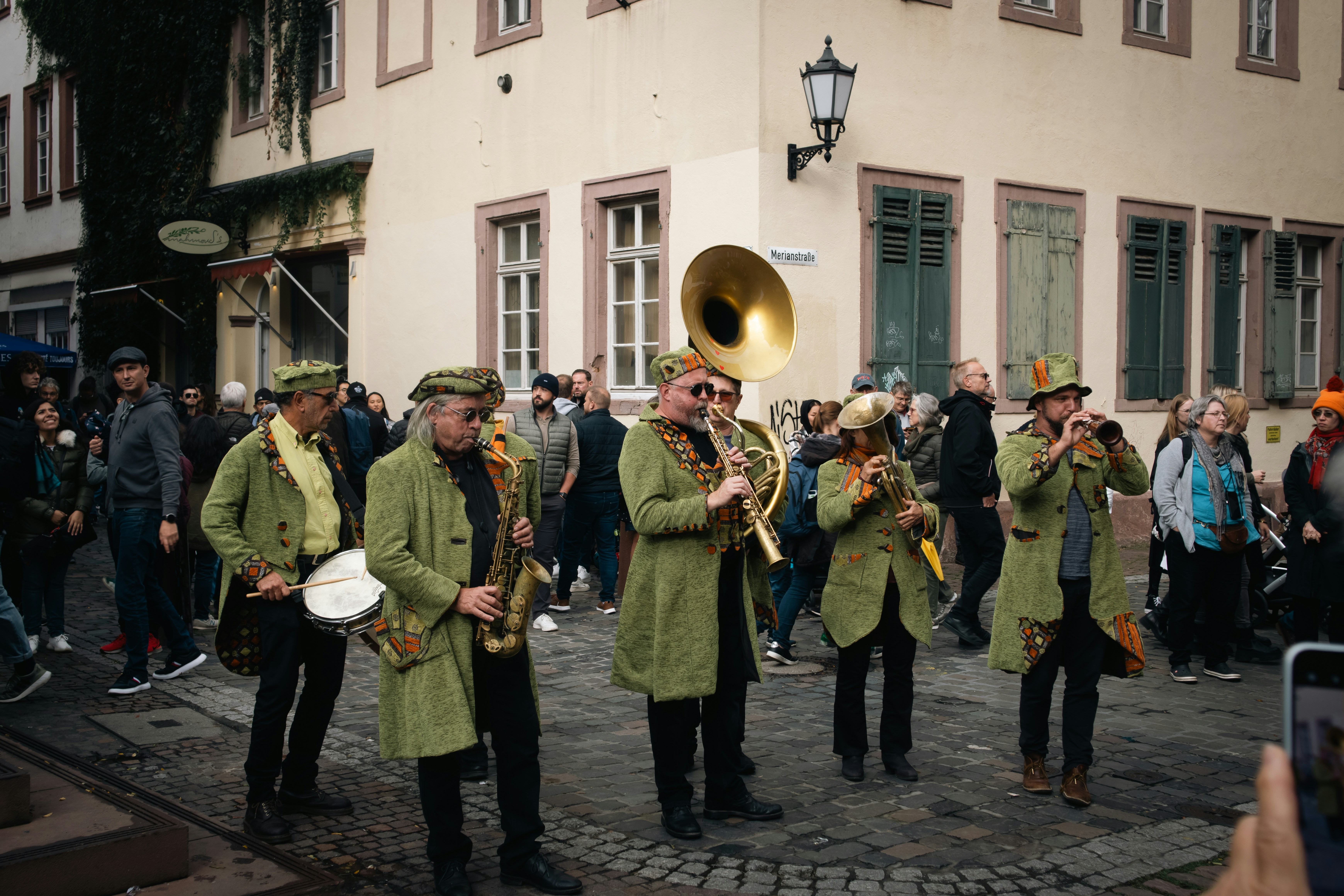 Green-coated brass band at a cobbled European street festival