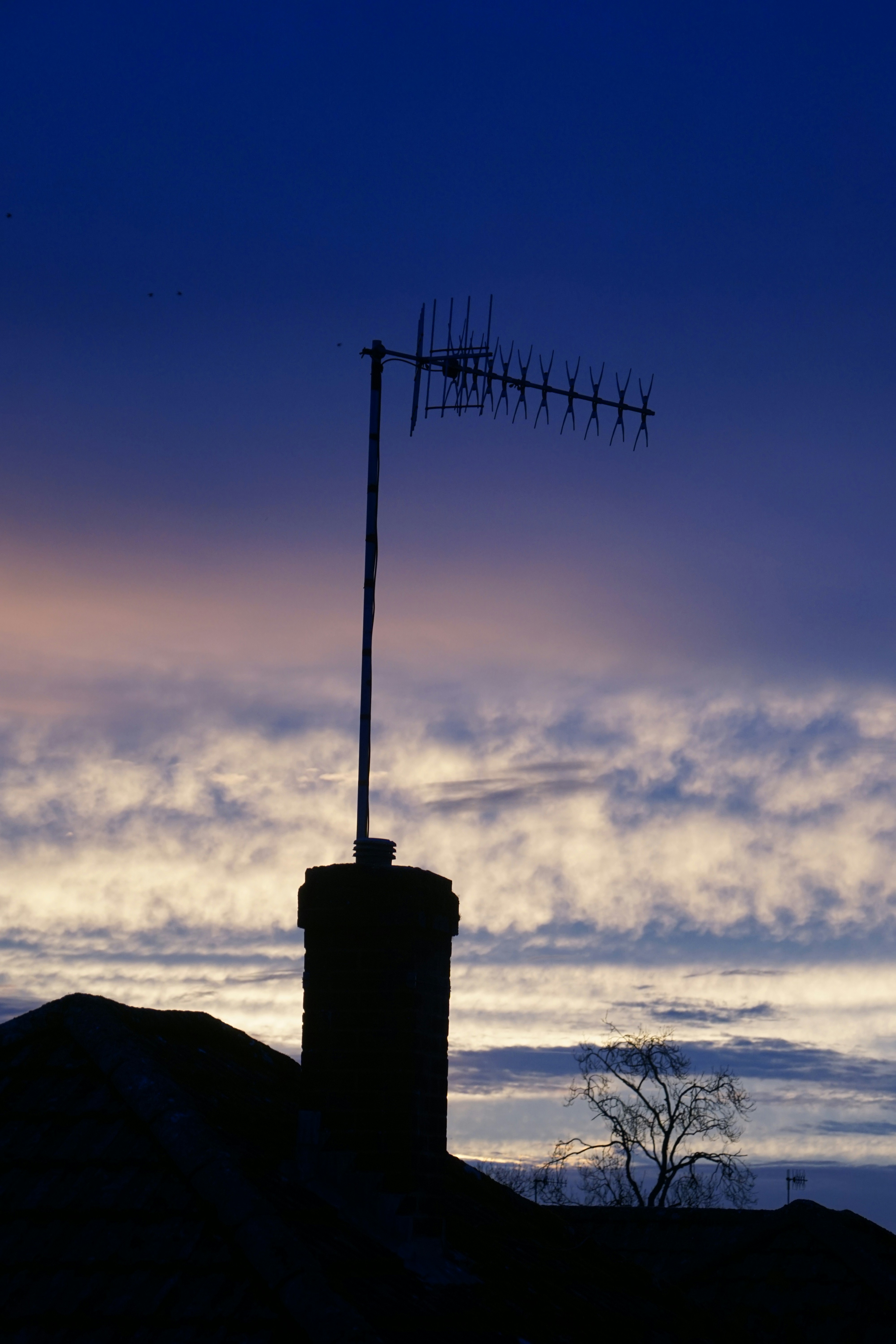 Silhouette of a rooftop antenna reaching toward a twilight sky
