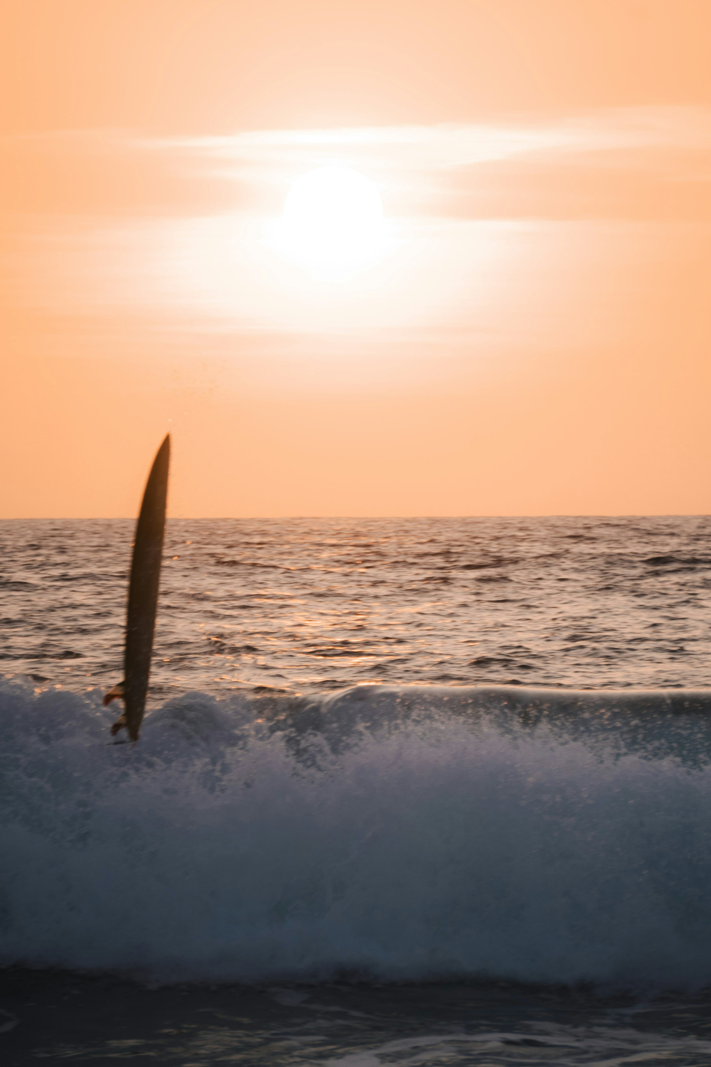 Sunlit surf and a lone surfboard silhouette at sunset
