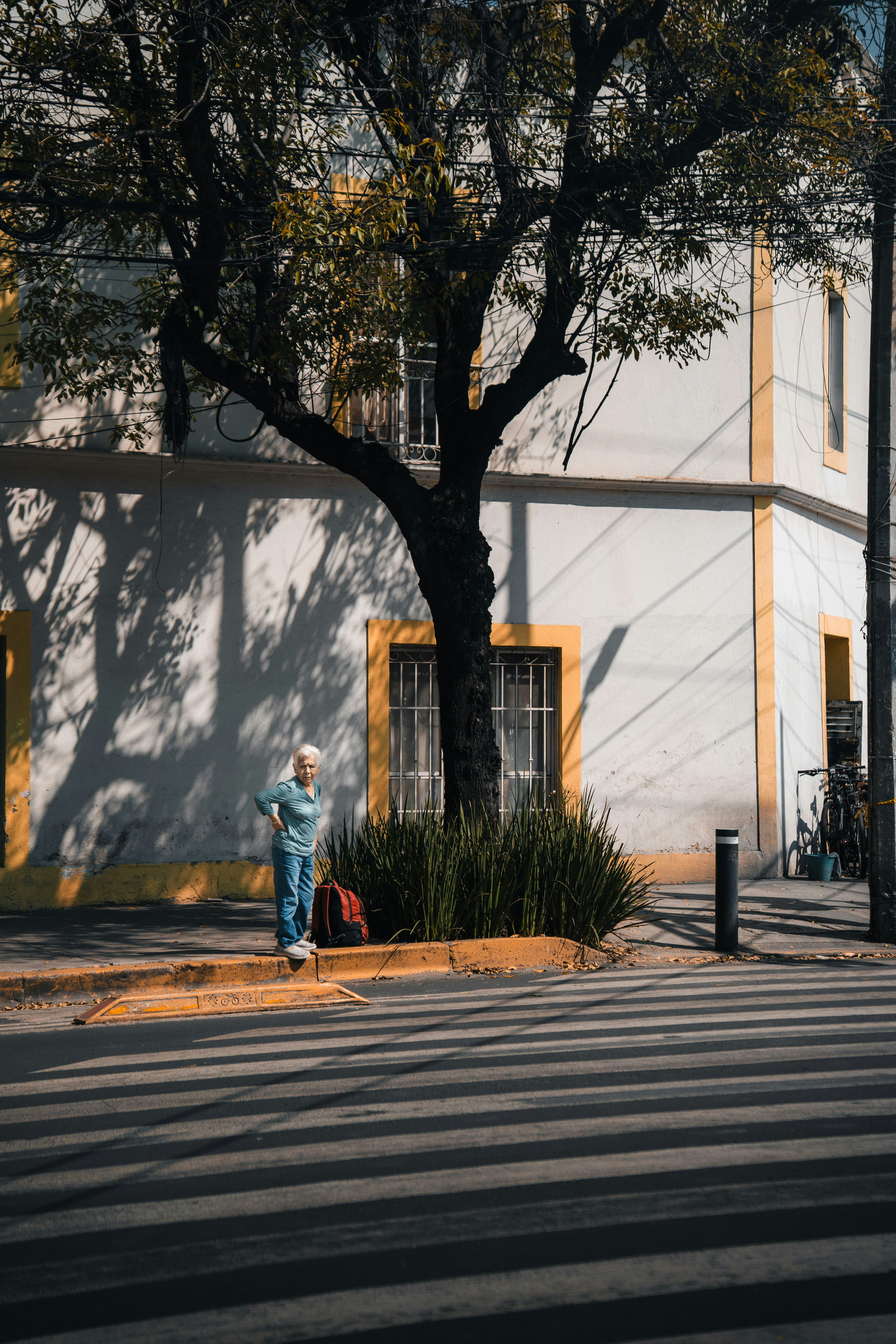 Orange-trimed wall, shadowed street, and a lone figure with backpack