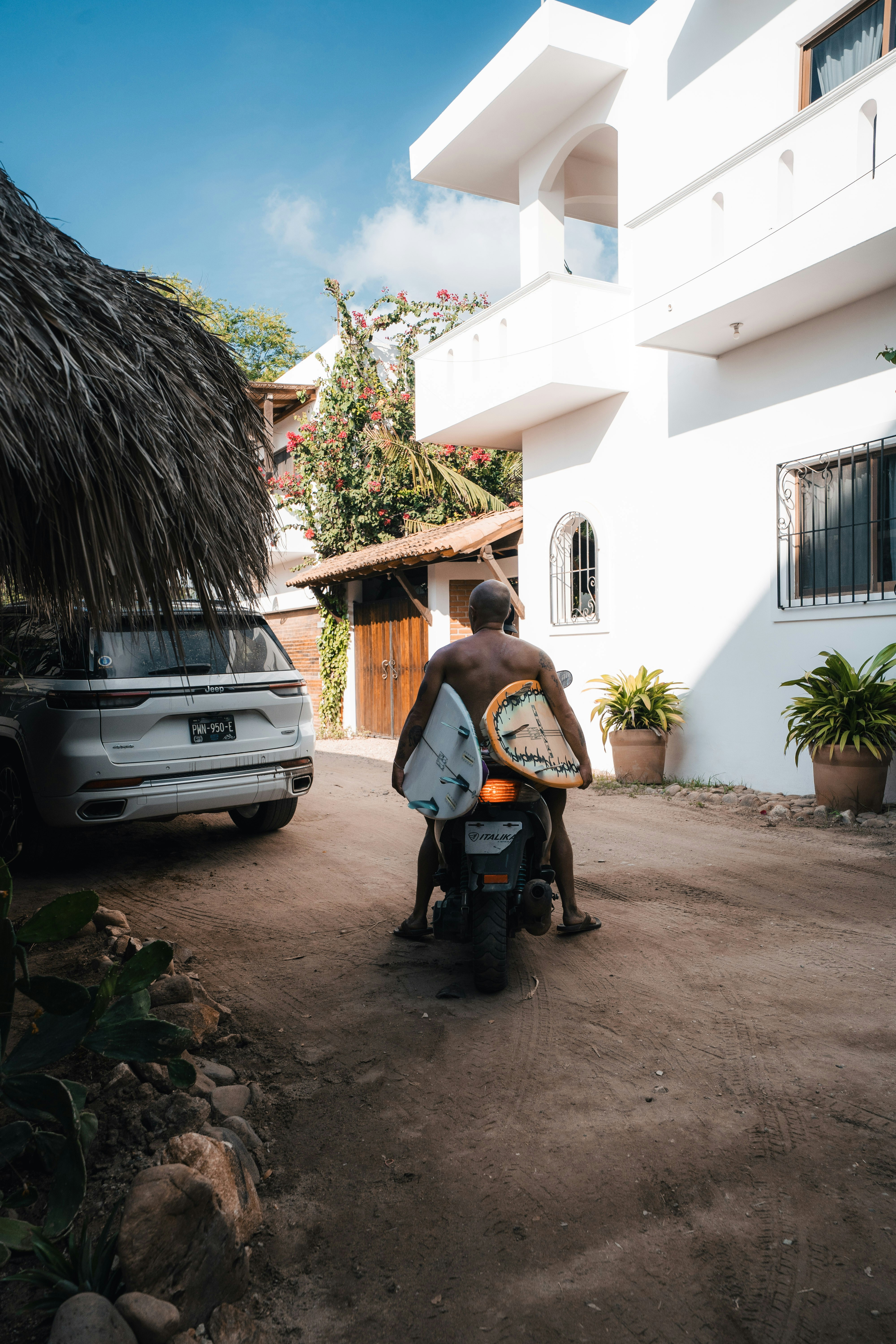 Sunlit Street Ride: A Surfer on Wheels Under a Coastal Villa