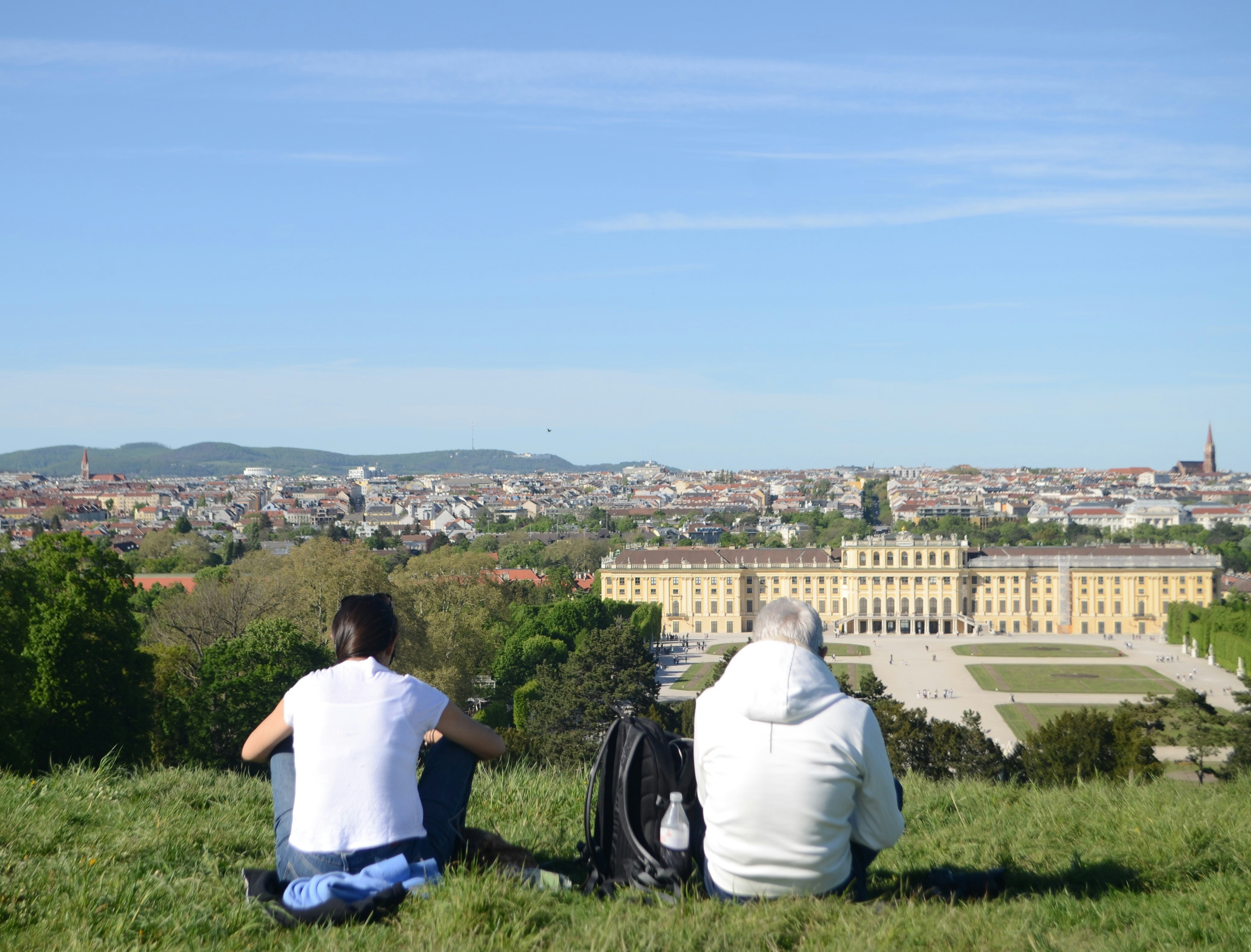 Two hikers overlook a sunlit city from a grassy hill