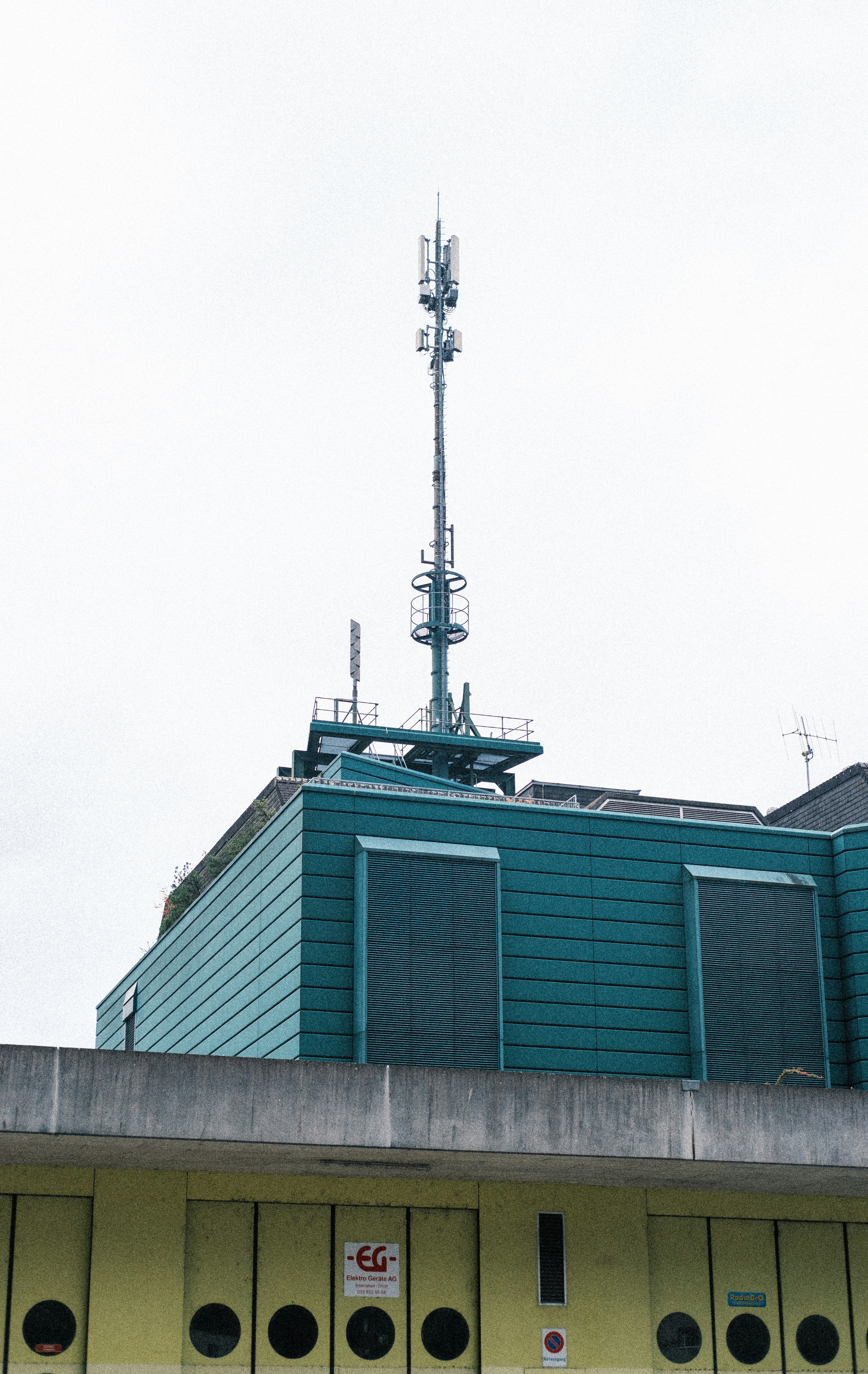 Rooftop Mast: A Mid-Tore Antenna Silhouette Over a Teal Facade