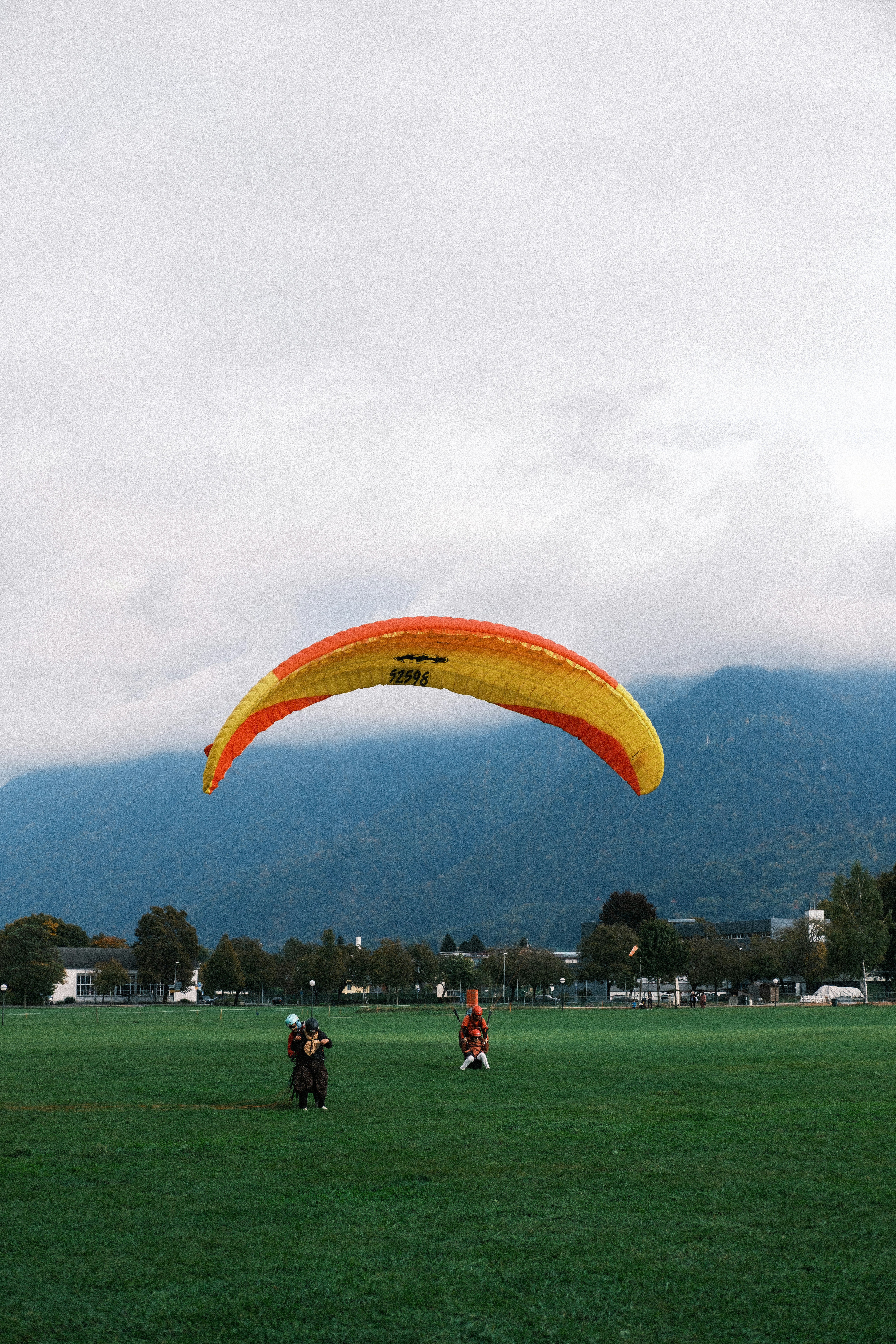 Red-Orange Paraglider over Open Field at Base of Mountain Range