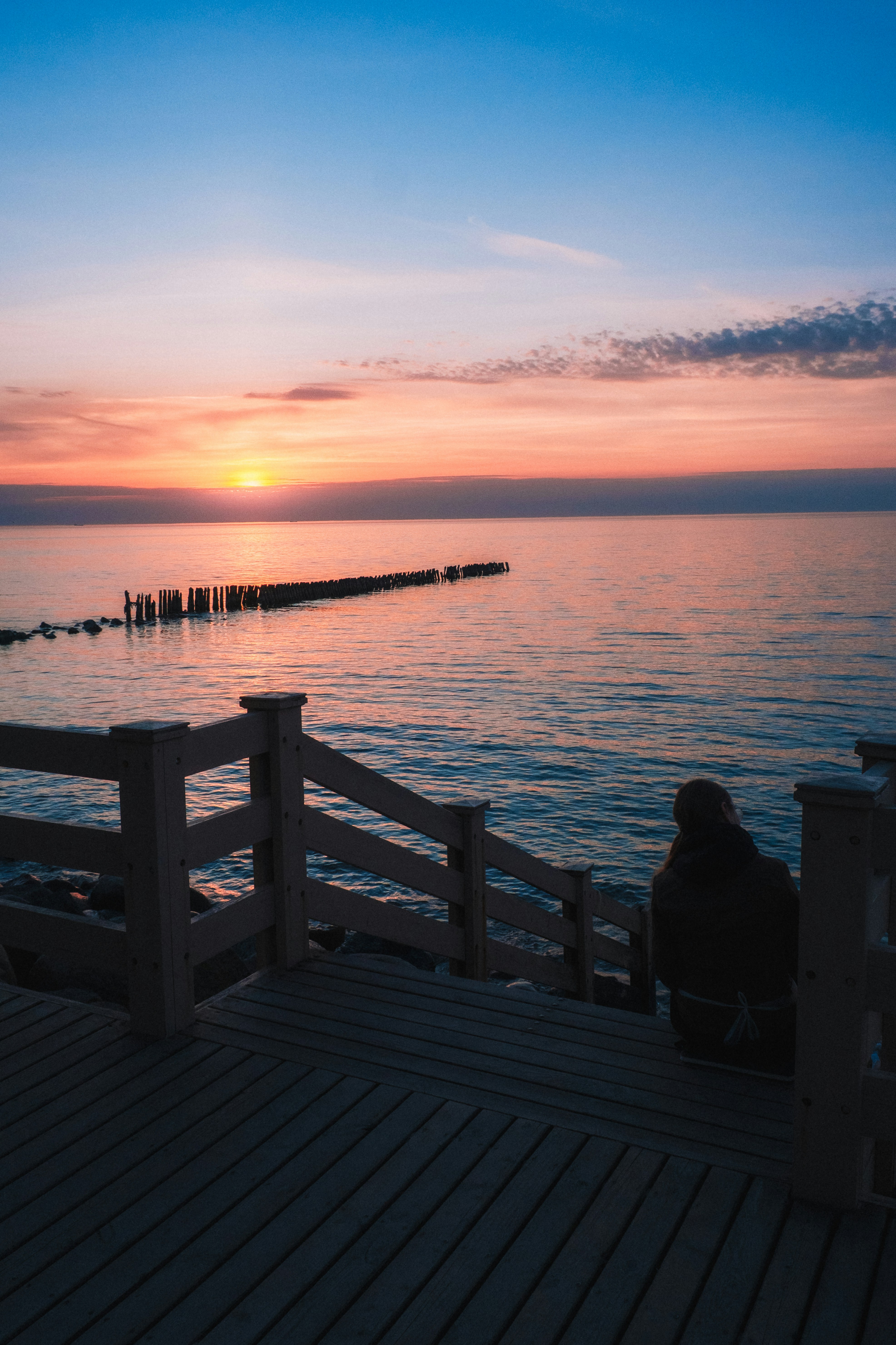 Sunset Over a Quiet Pier: A Solitary Figure and the Distant Breakwater