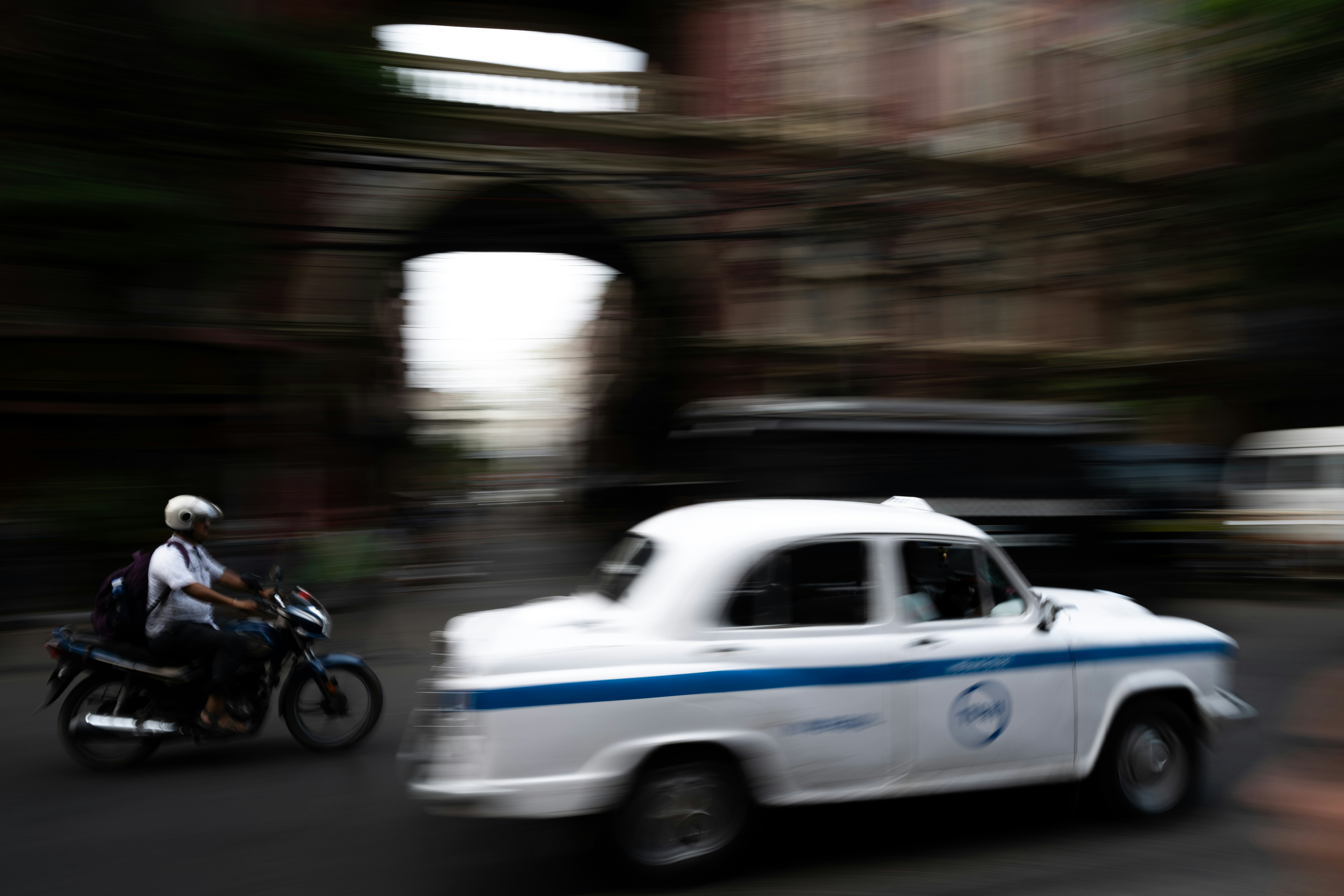 Blurry pursuit: a police car and motorbike race through a shaded city archway