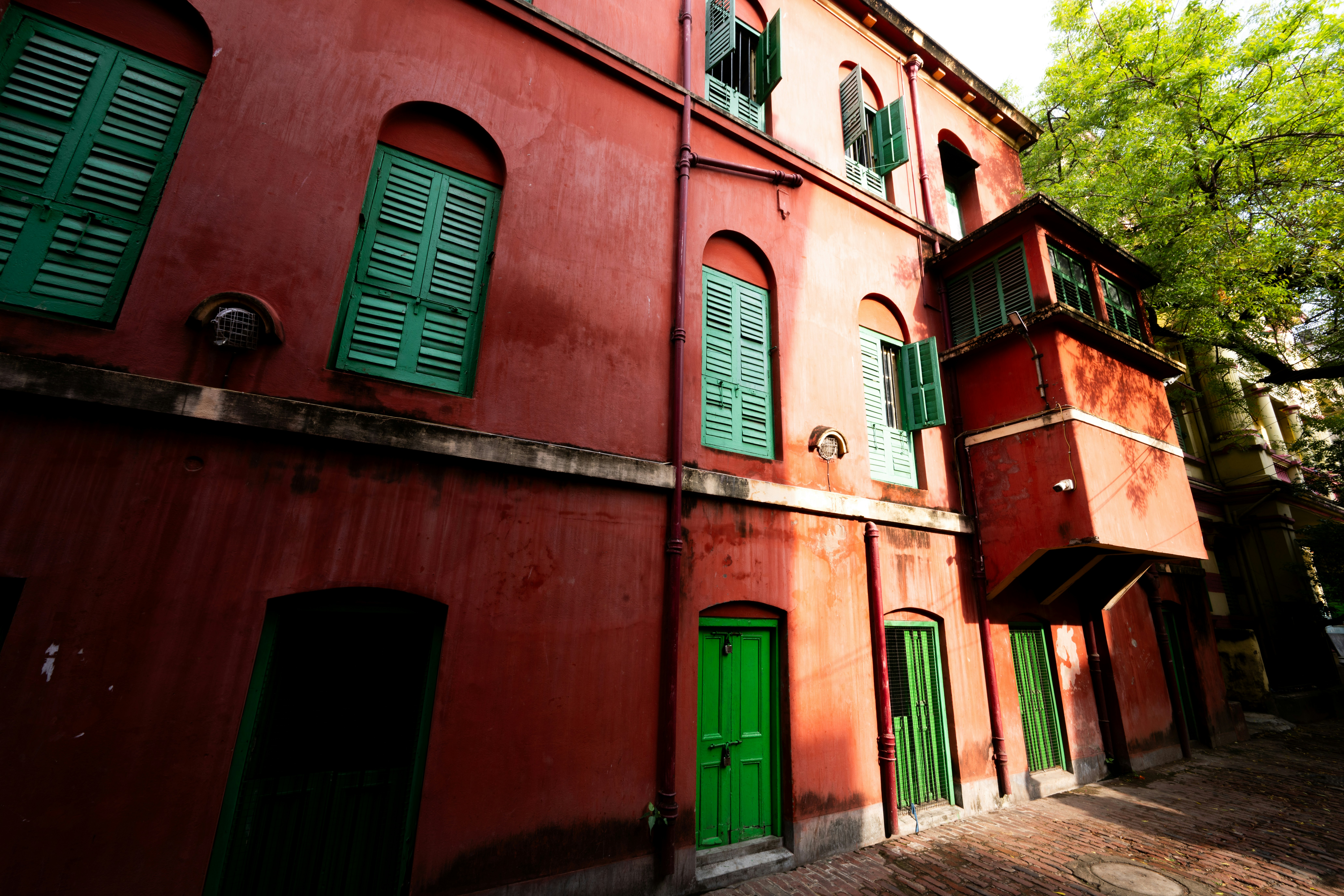 Red Facade with Green Doors: A Sunlit Alley of Shuttered Windows