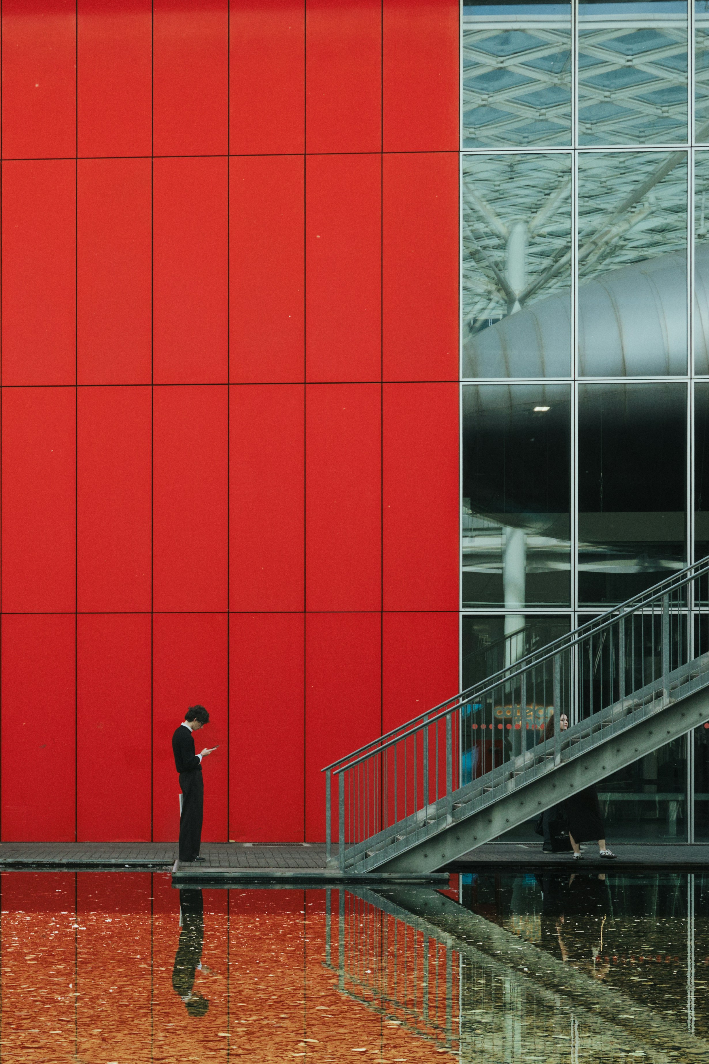 Red Facade, Silent Figure: A Quiet Moment by the Glass and Stairs