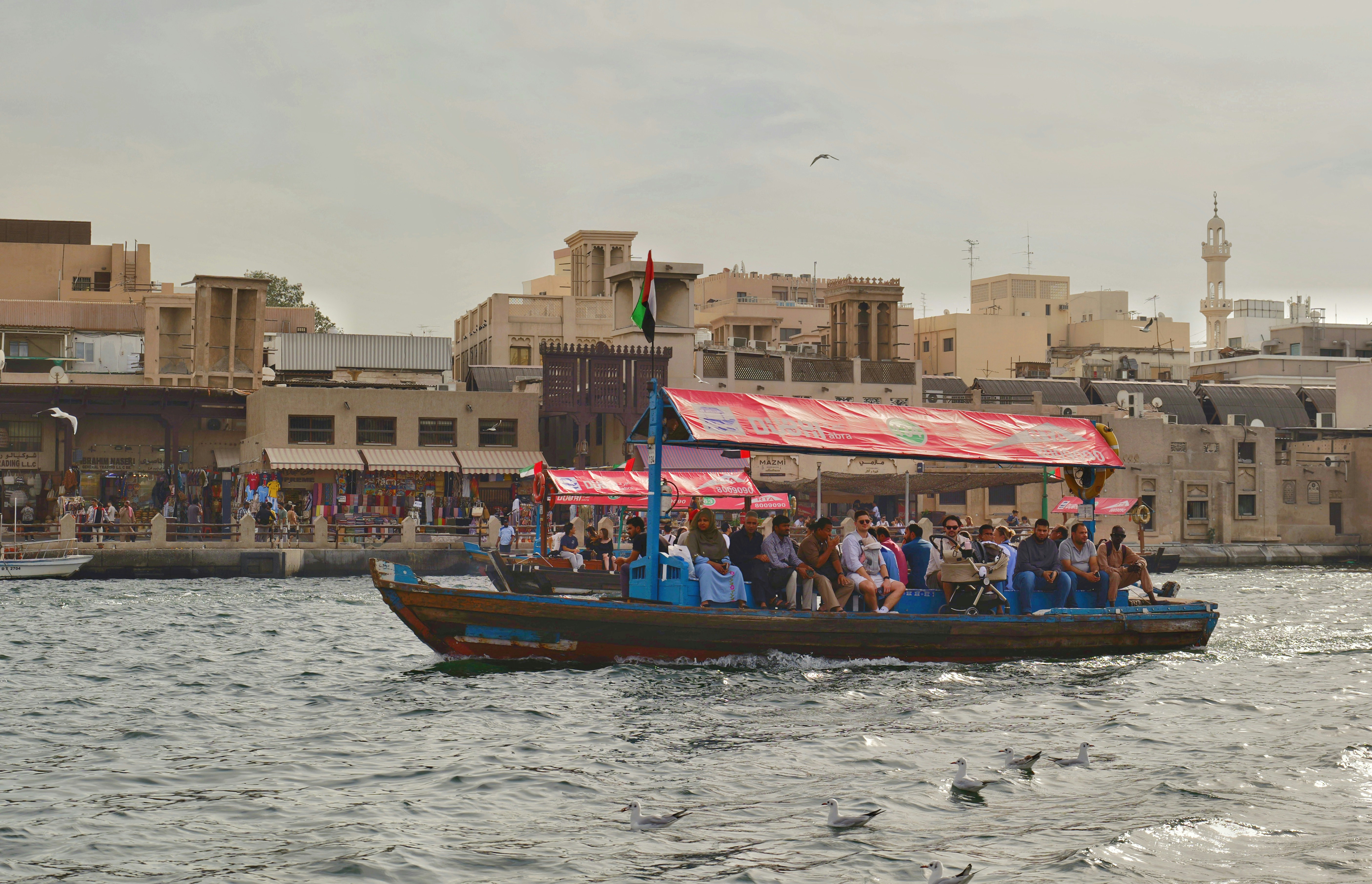 Blue-robed passengers on a river ferry glide past a historic harbor