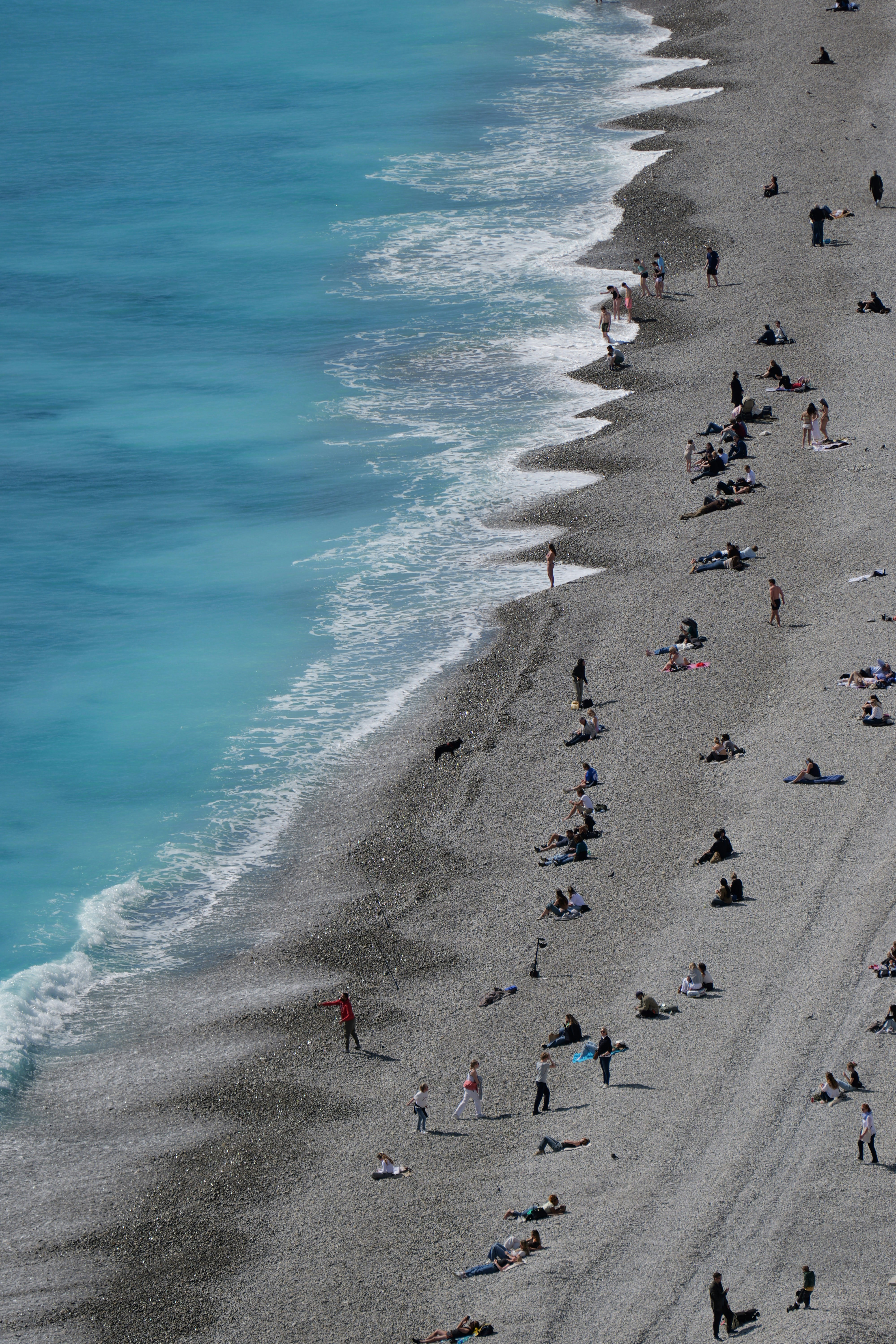 Azure shoreline crowd: Aerial view of sunseekers along a pebbly Mediterranean coast