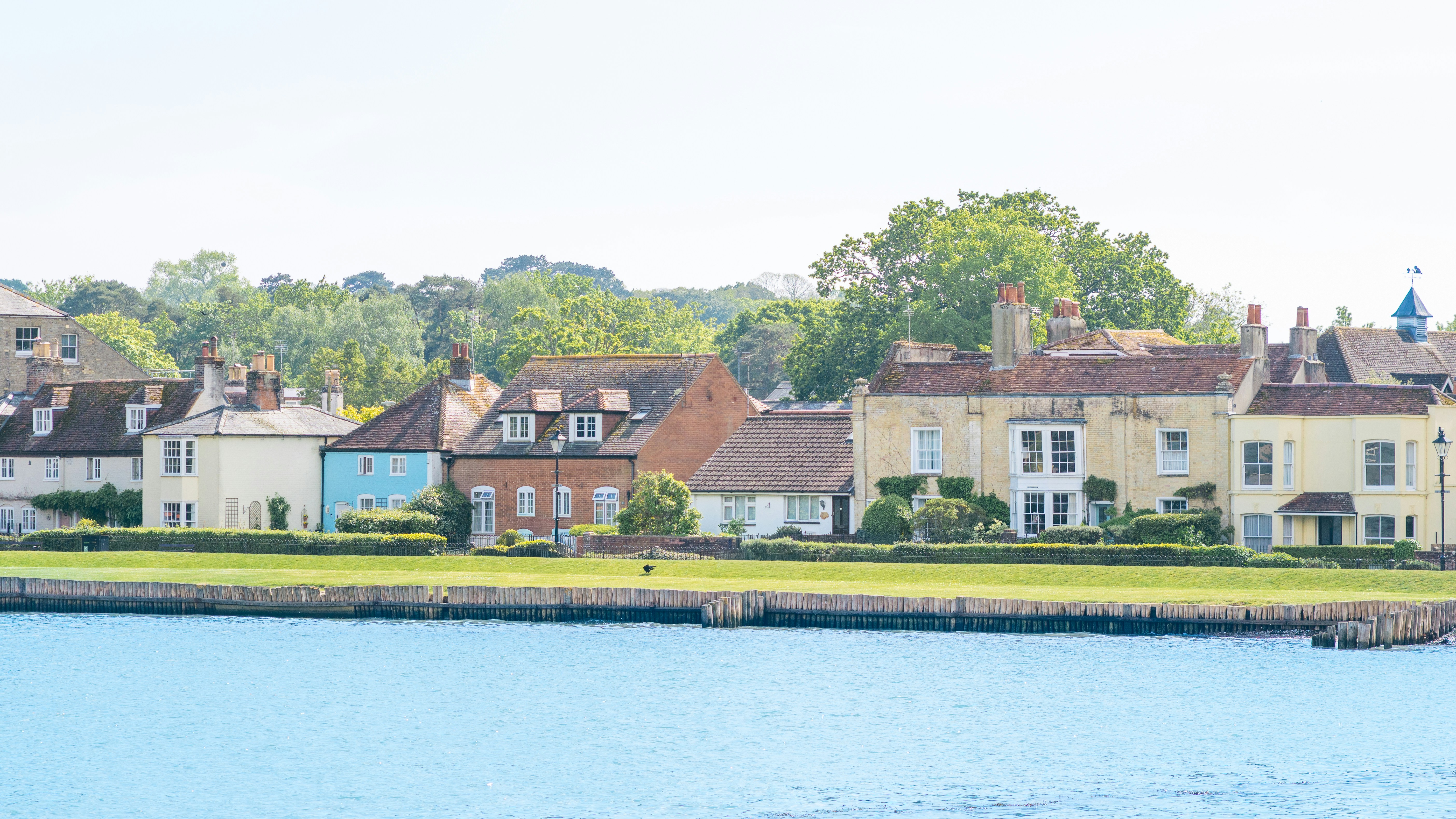 Colorful cottages line the waterfront with a calm blue water foreground and green lawns behind; a tranquil harbor scene with pastel houses and a clear sky.
