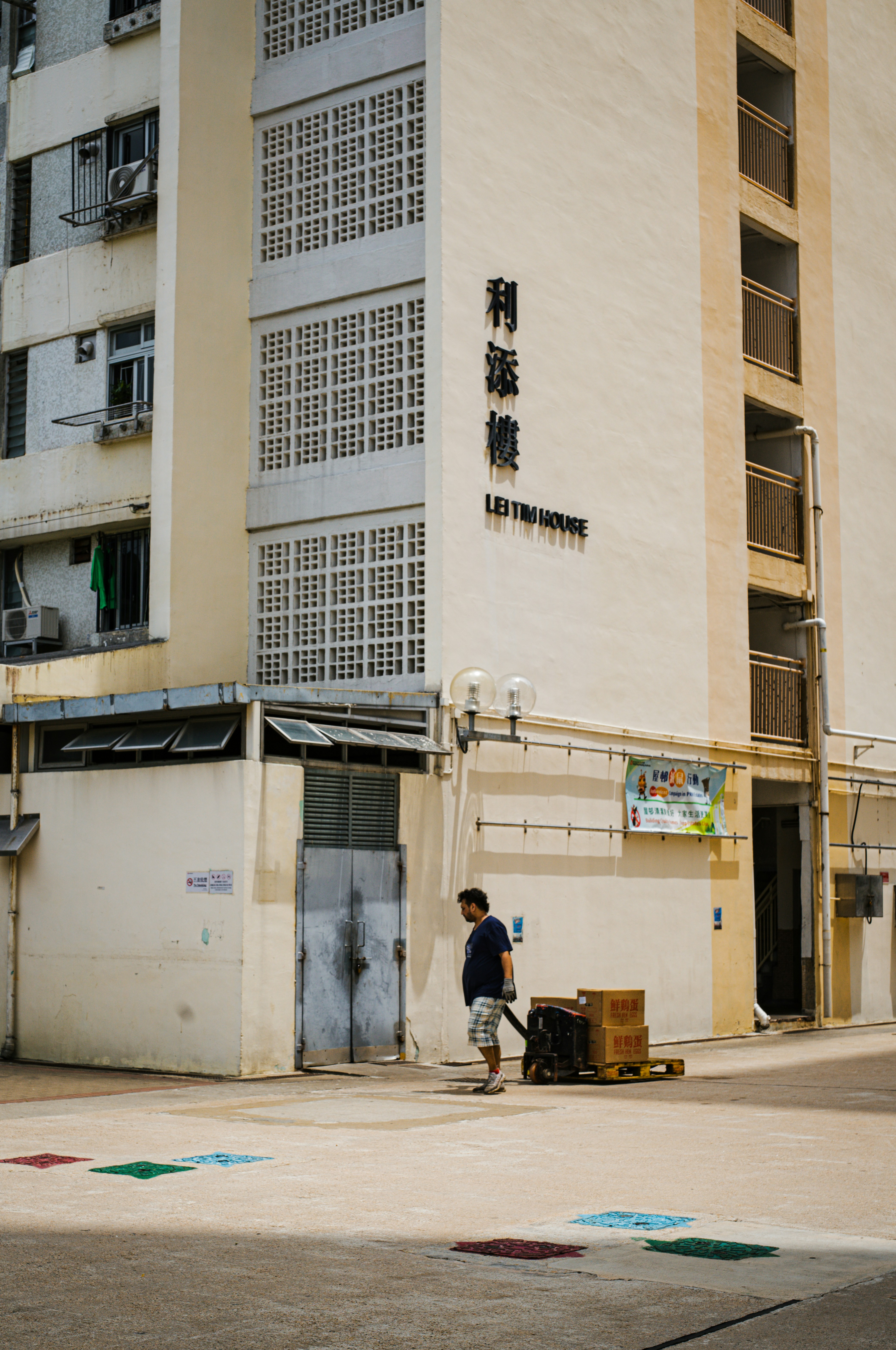 Narrow street scene beside a pale apartment block with a man and a small cart on the sidewalk.