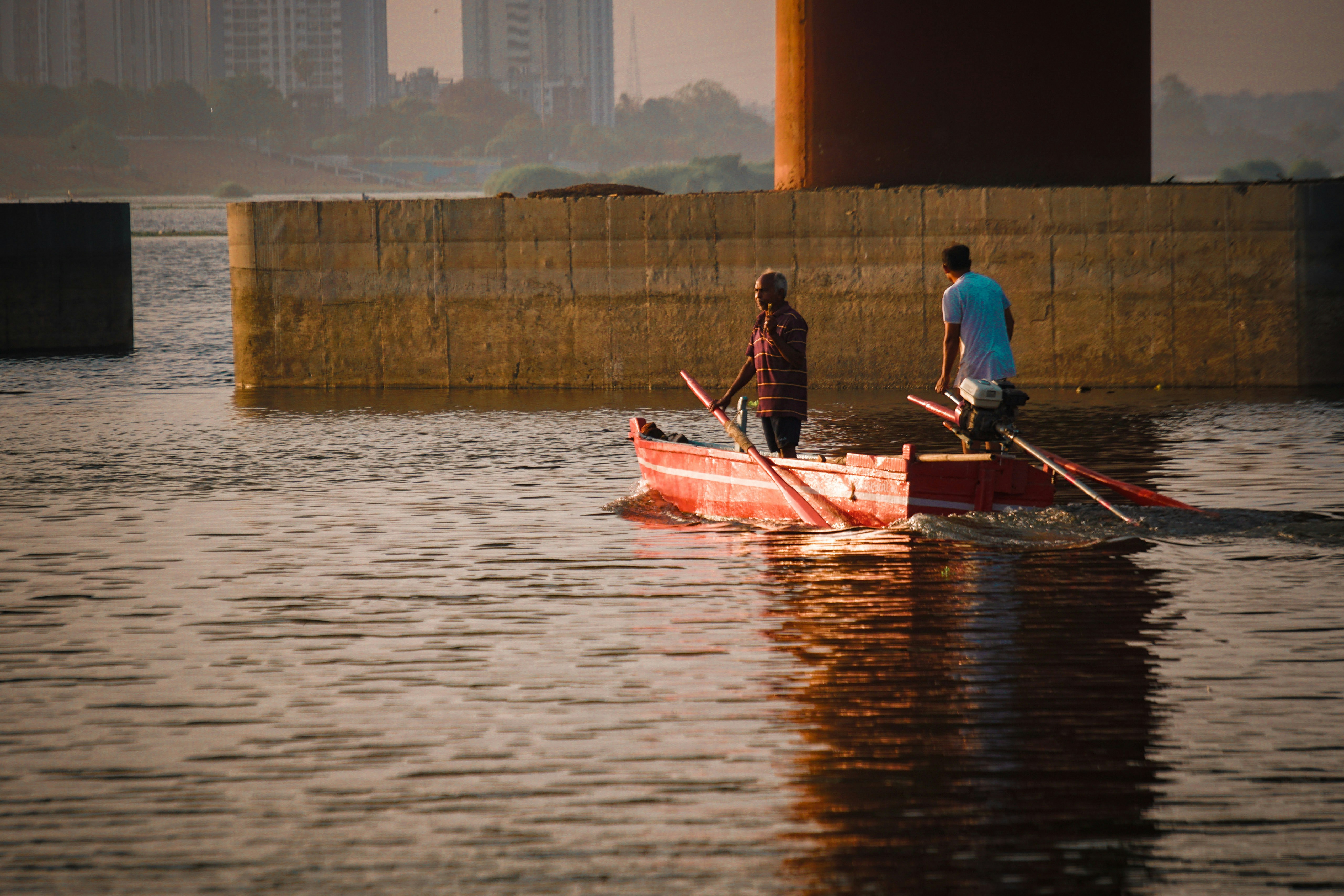 Rower duo beneath a sun-warmed industrial jetty casting reflections on calm harbor waters