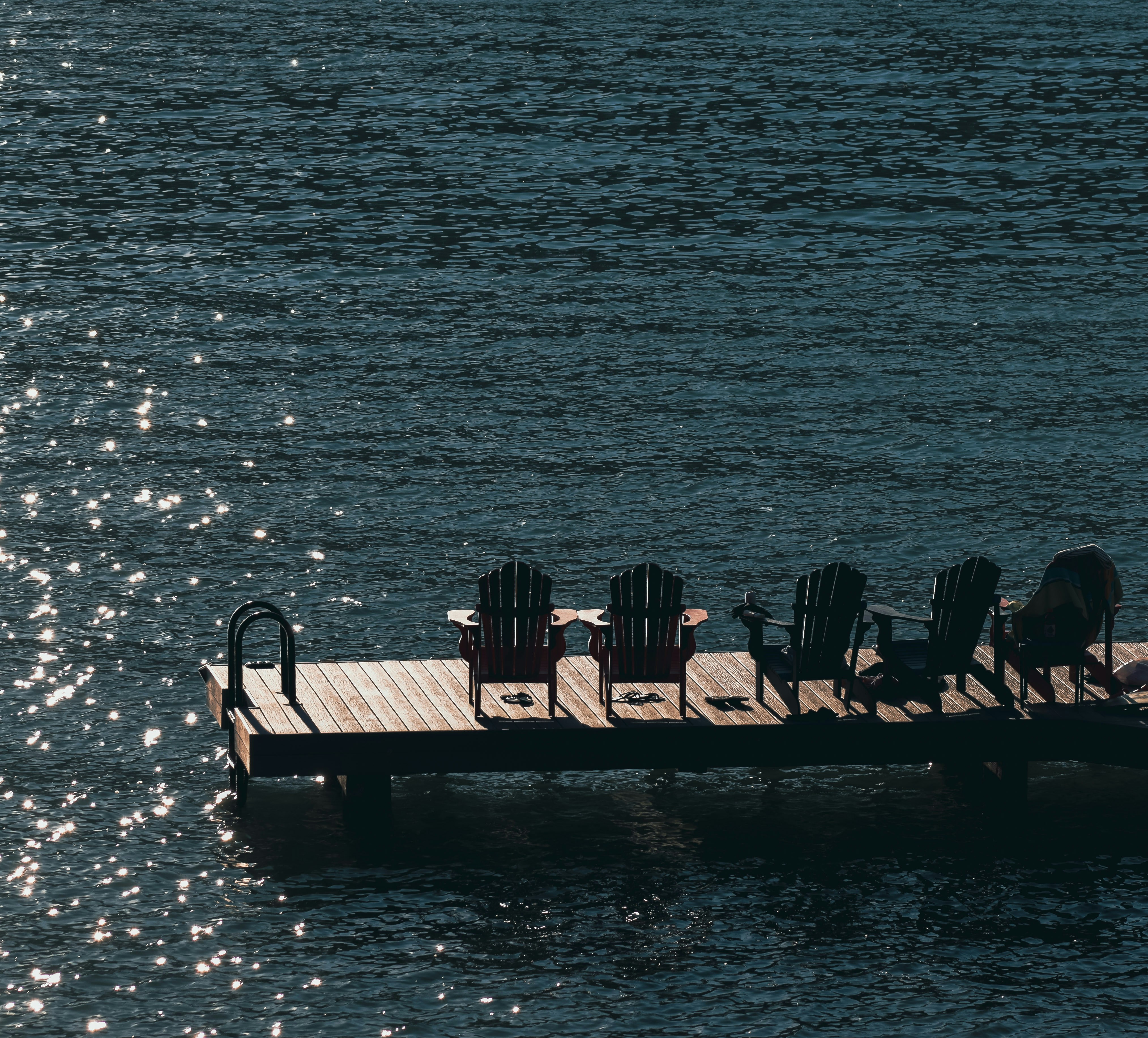 Sunlit Pier: Quiet Row of Adirondack Chairs on a Sparkling Lake
