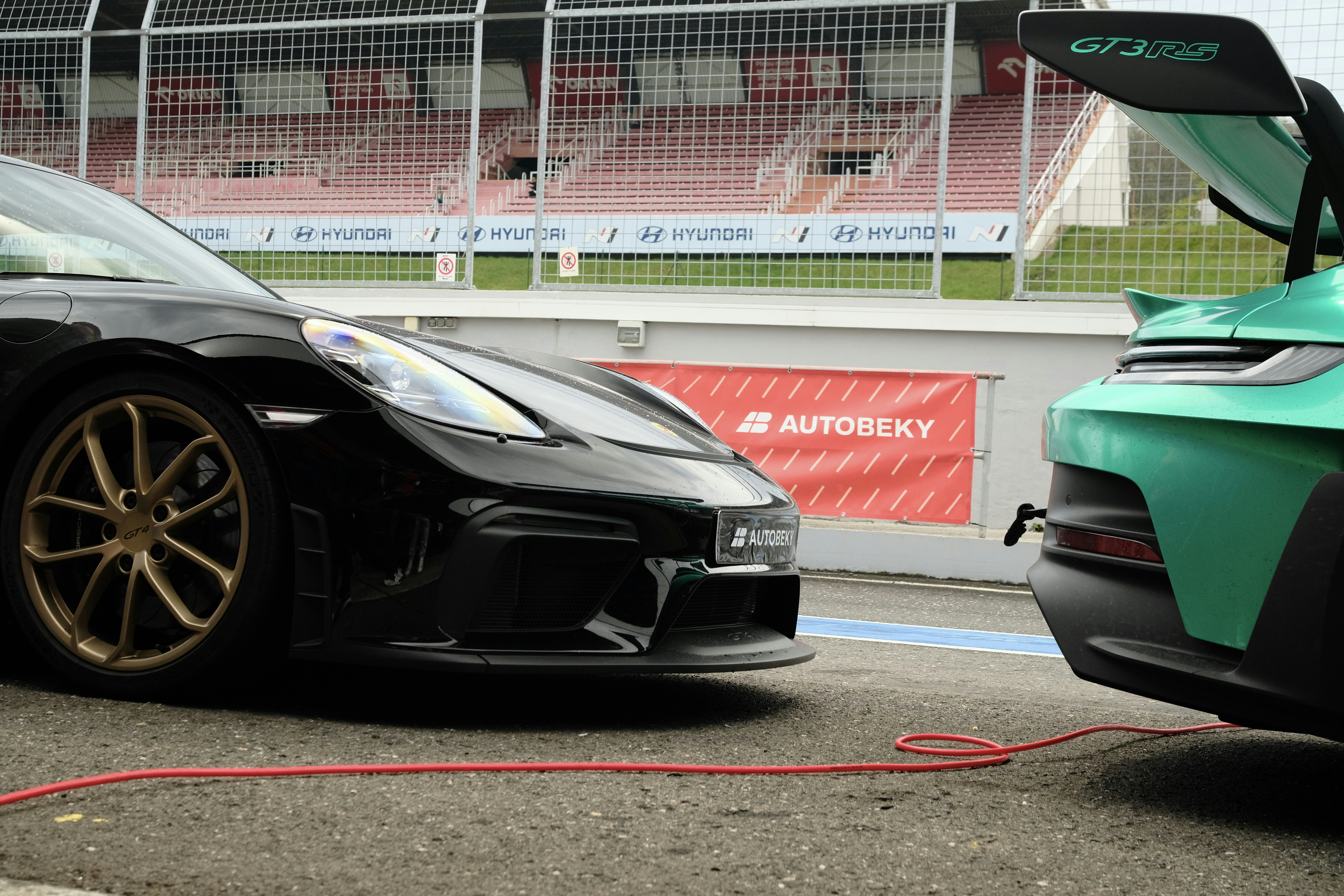 Low-angle duel: black sports car and green rear in a pit-stop scene