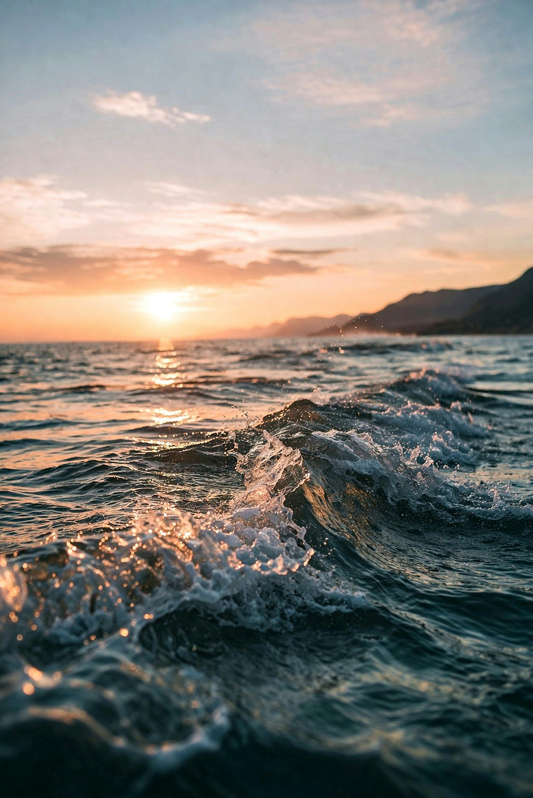 Sunlit Crest: Ocean Waves Rolling Toward a Distant Shore at Dusk