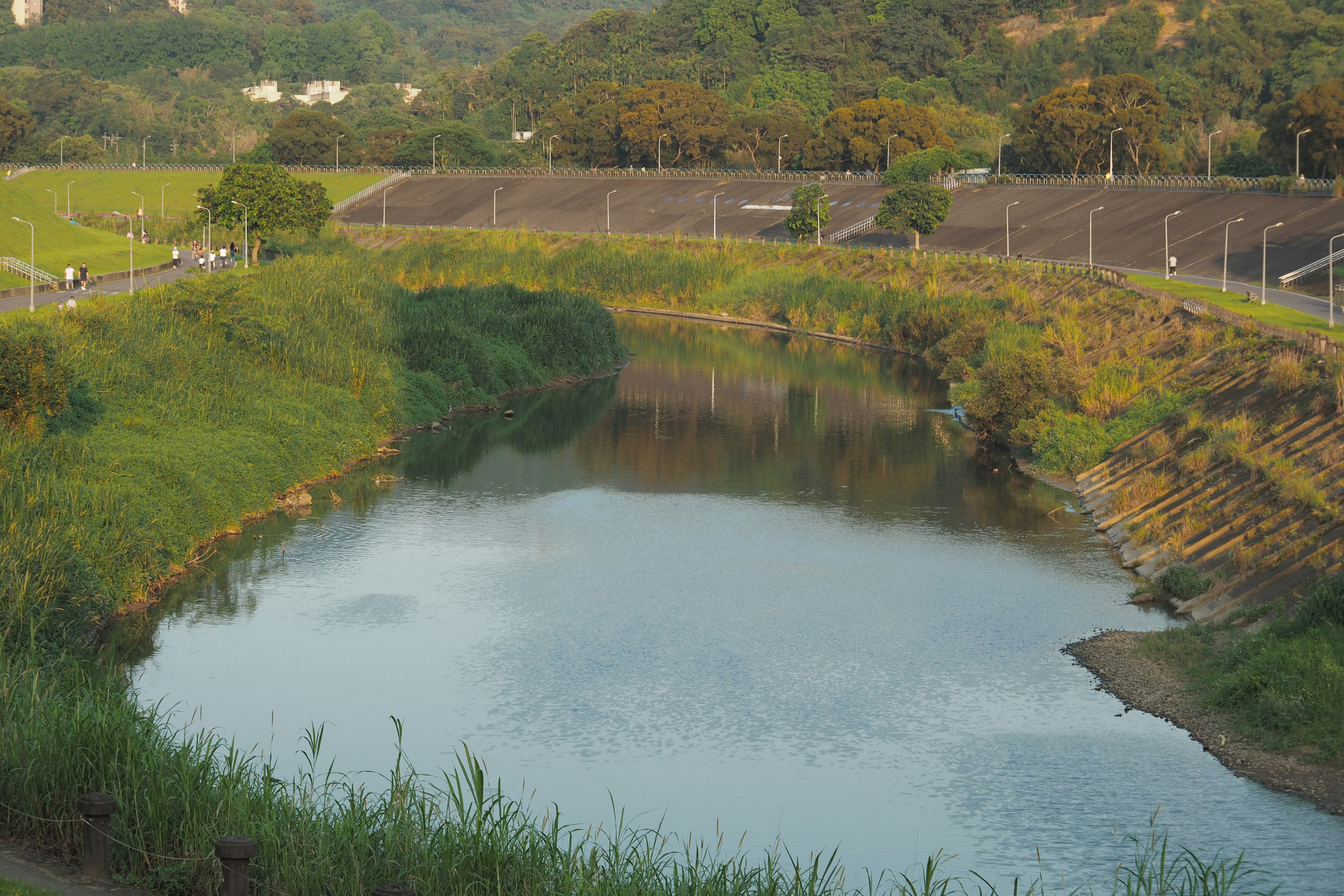 River corridor with grassy embankments and a distant walkway