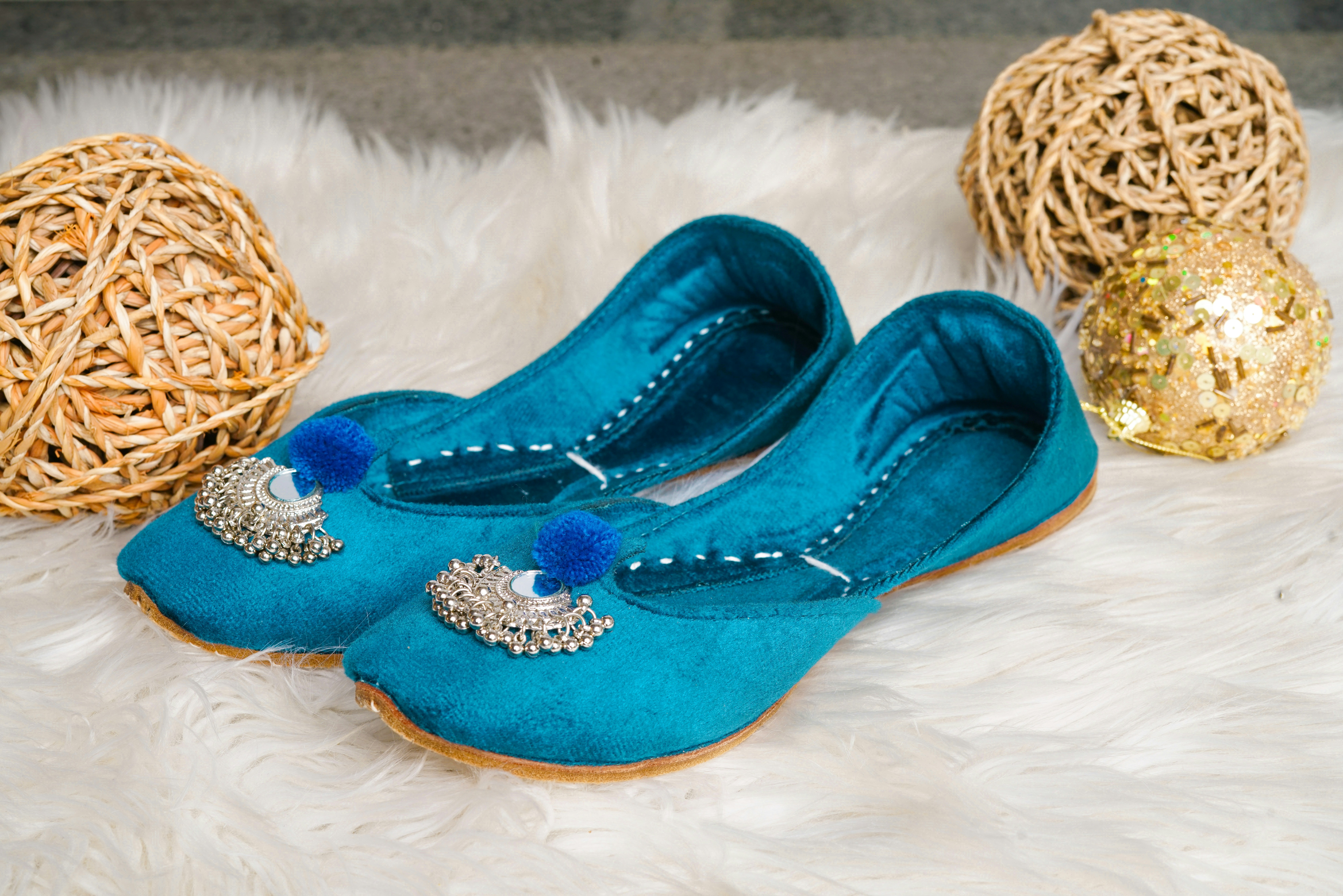 Blue velvet flats with decorative beads sit on a fluffy white background, framed with natural decorative spheres. A simple still life emphasizing color, texture, and light.