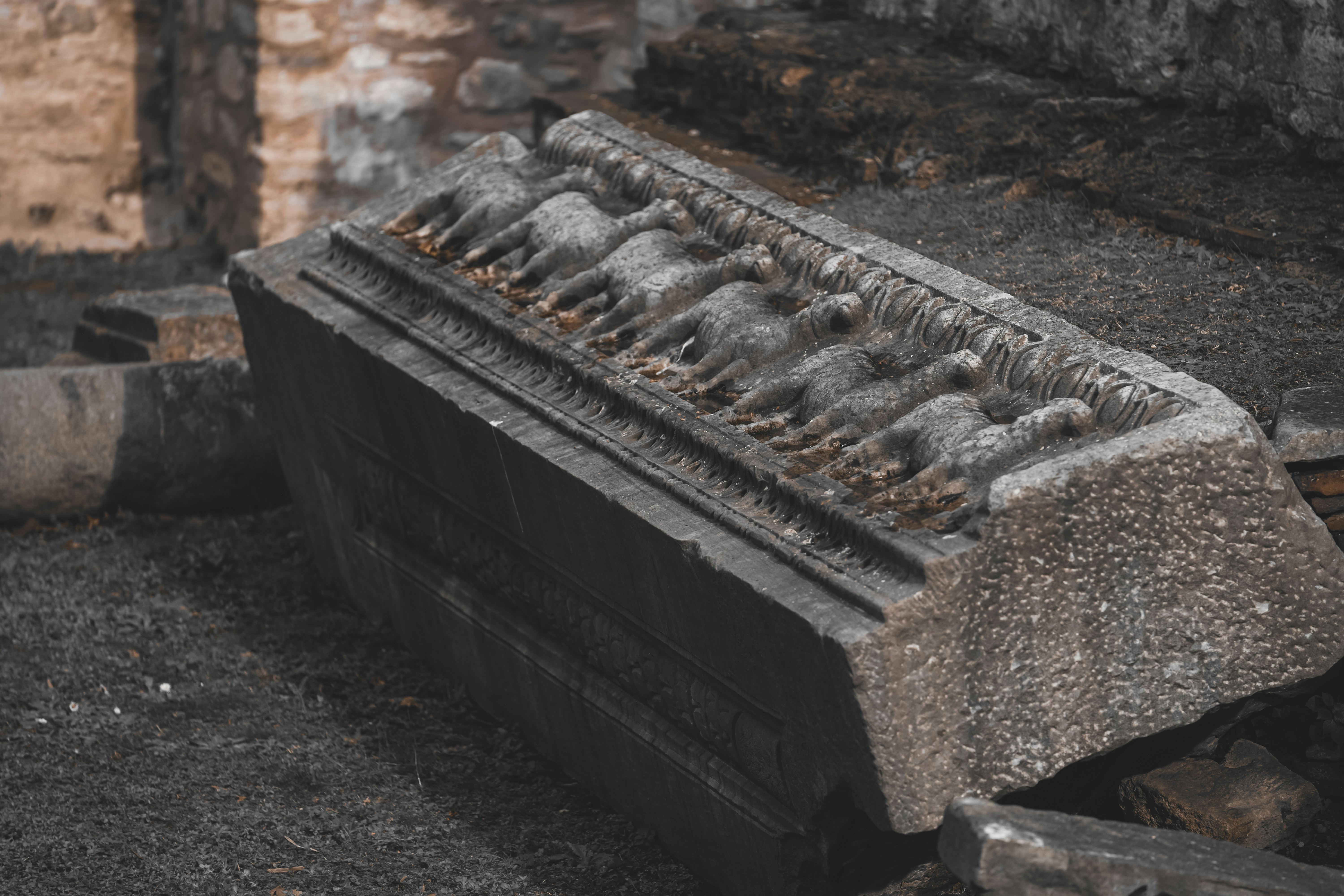 Ruined pedestal stone with carved grooves rests among dark rubble
