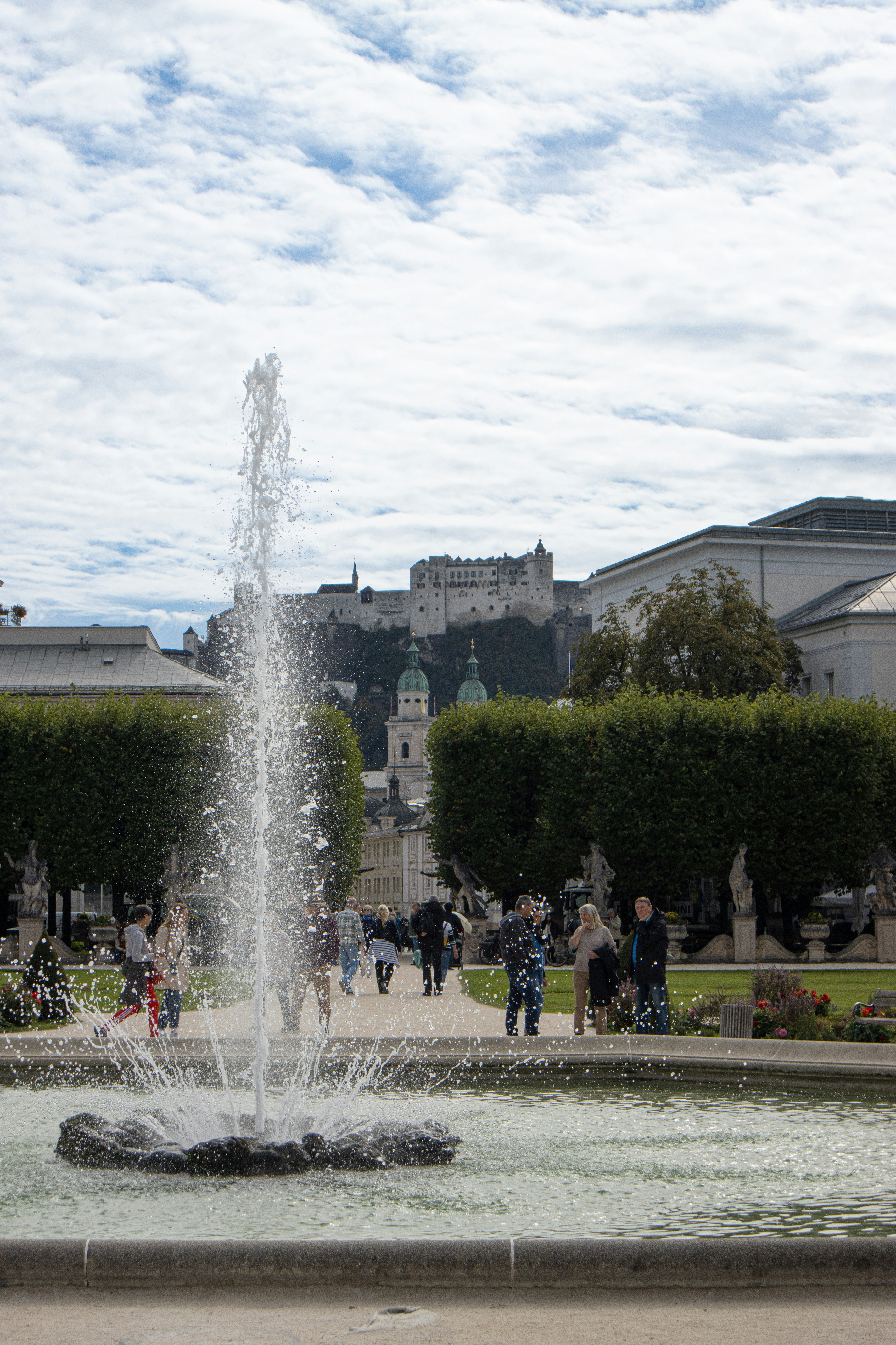 Jet of water with historic skyline: a sunlit city fountain framed by visitors