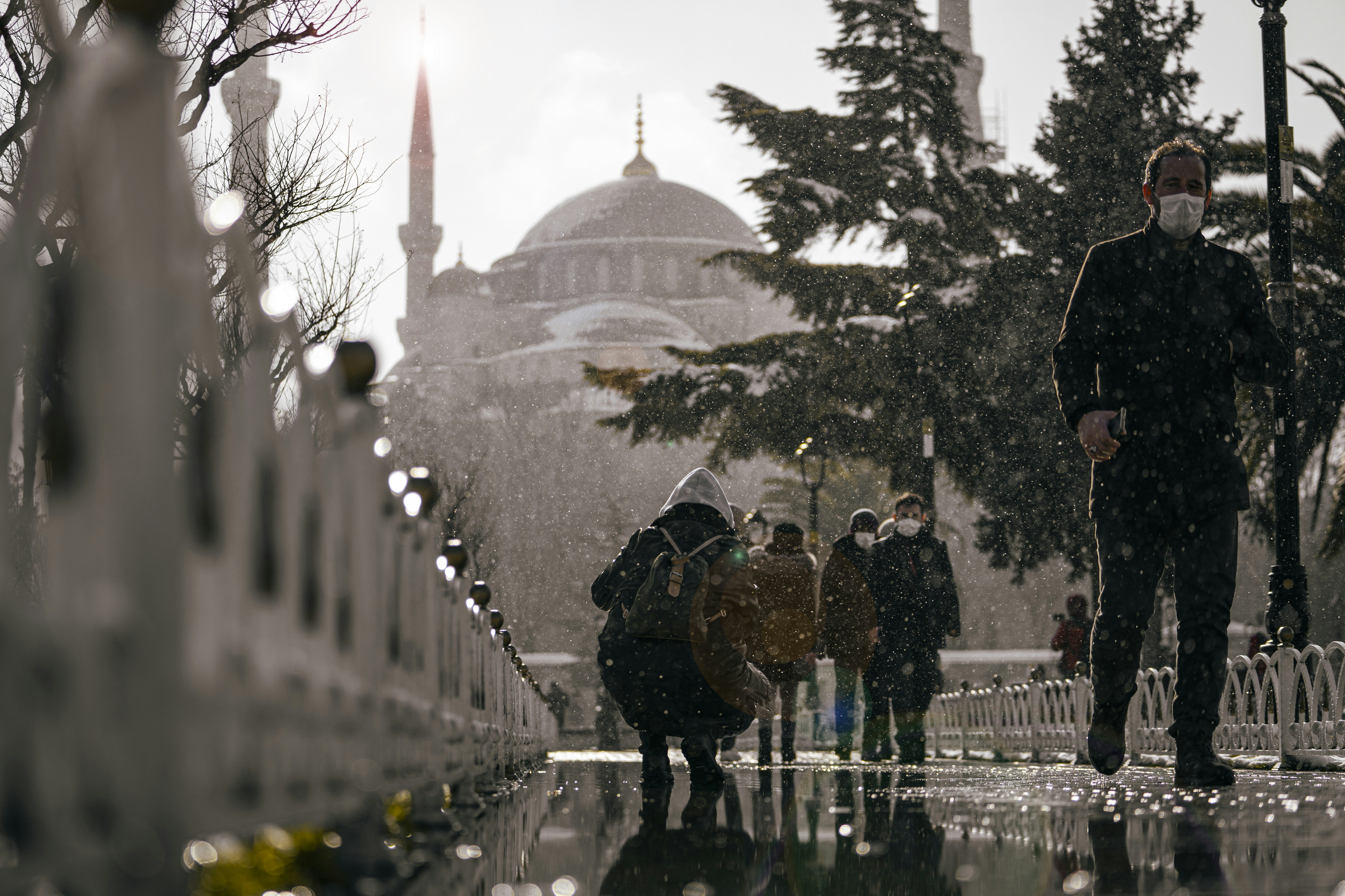 Snowy Footpath Amid People in Masks With Mosque in Background