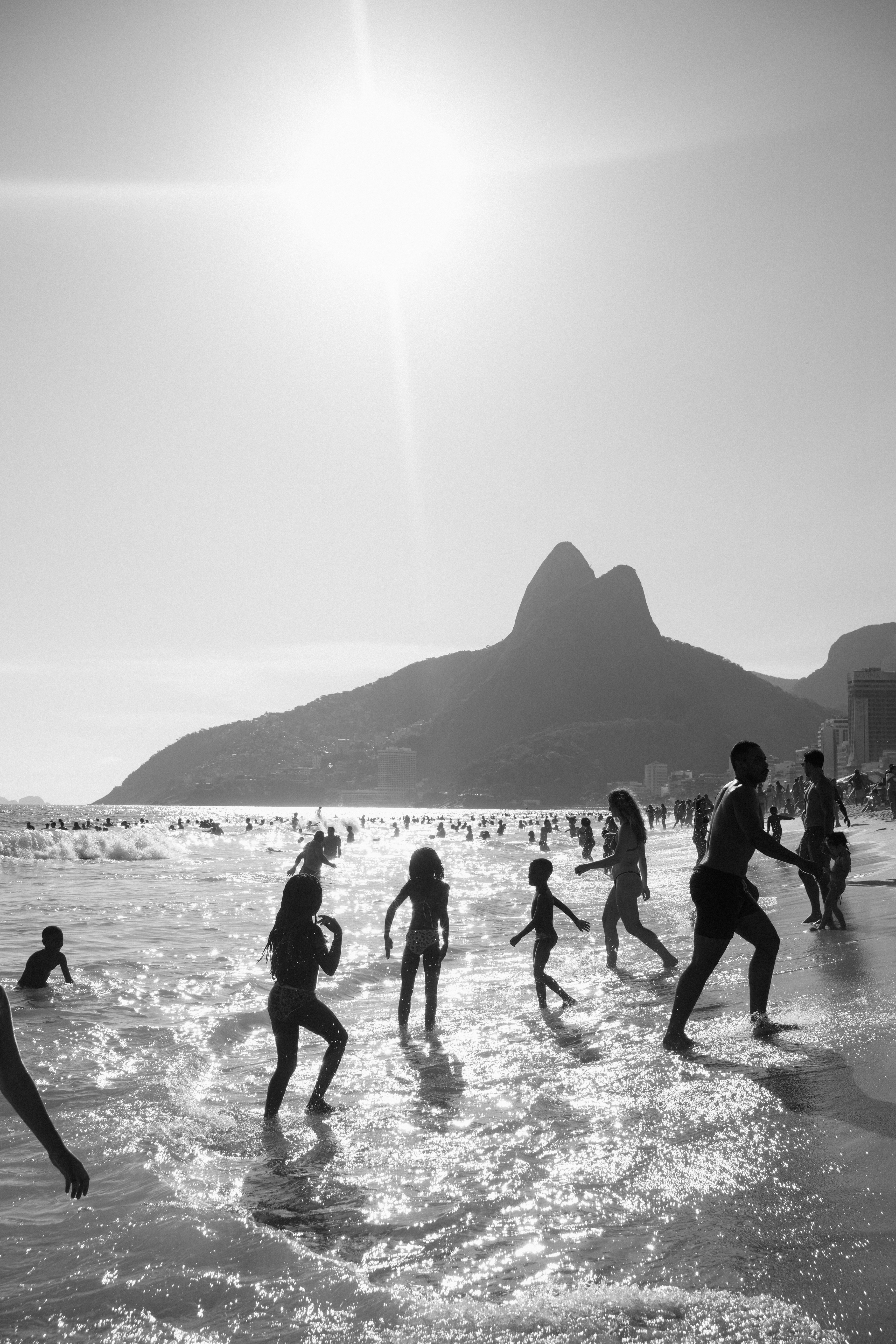 Sunlit Shoreline: People Play Along a Brazillian-like Beach with Prominent Rock Outcrop