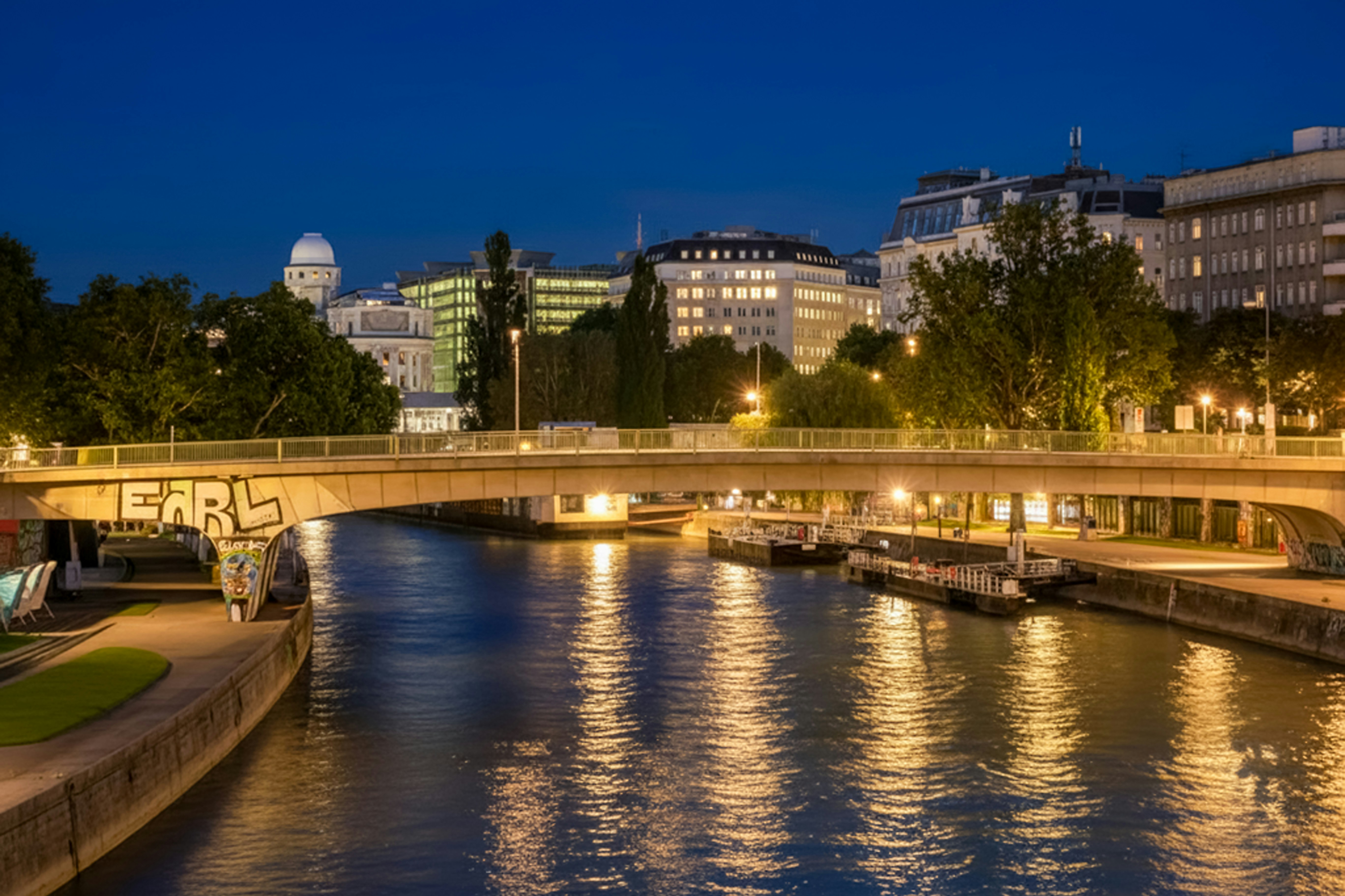 Evening Flow: City Lights Reflect on the Thames-like River Under a Calm Bridge