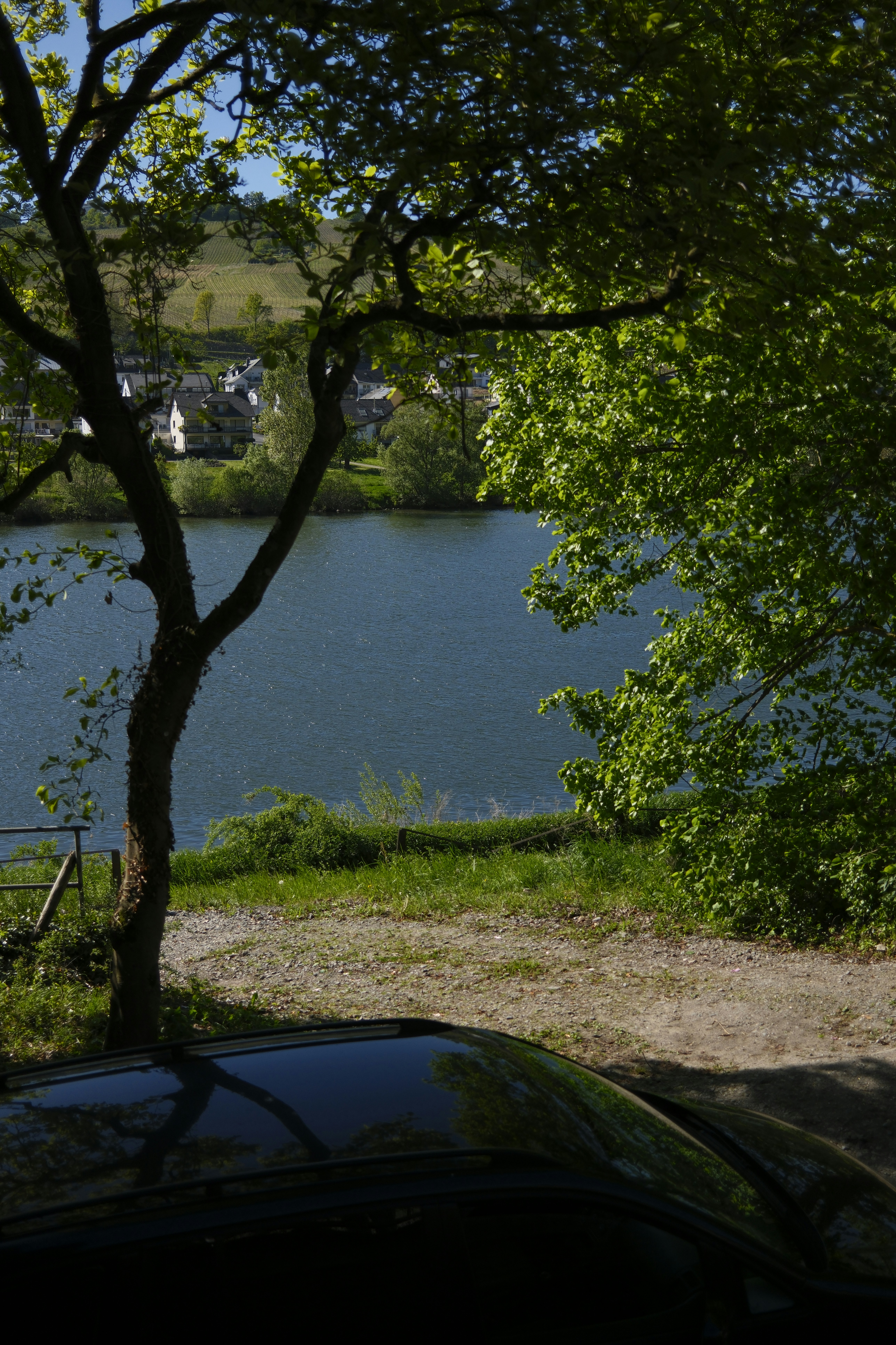 Shaded overlook by the river: car roof, tree frame, and distant village