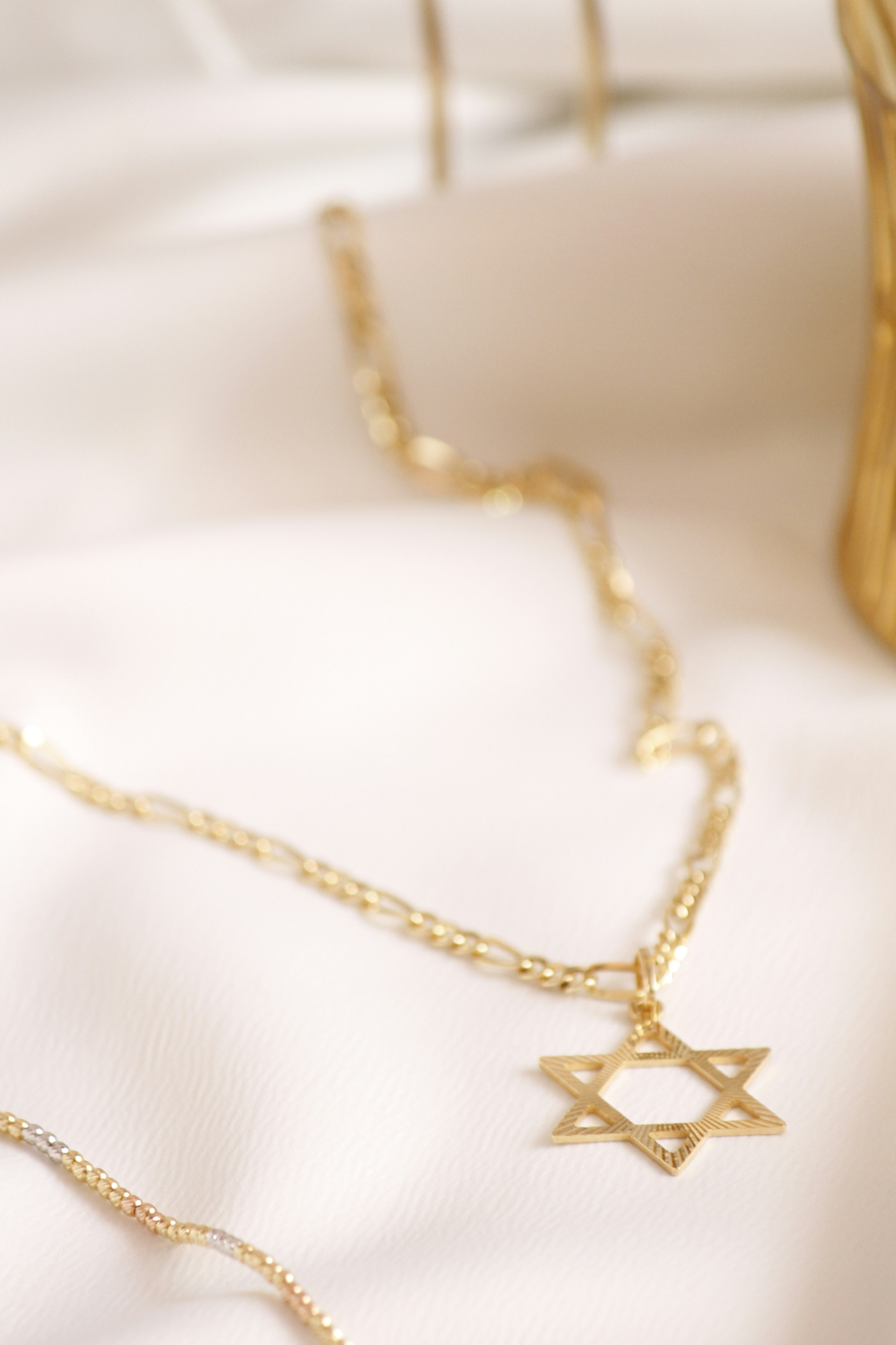 Star of Davids Shimmer: Gold Necklace resting on ivory fabric