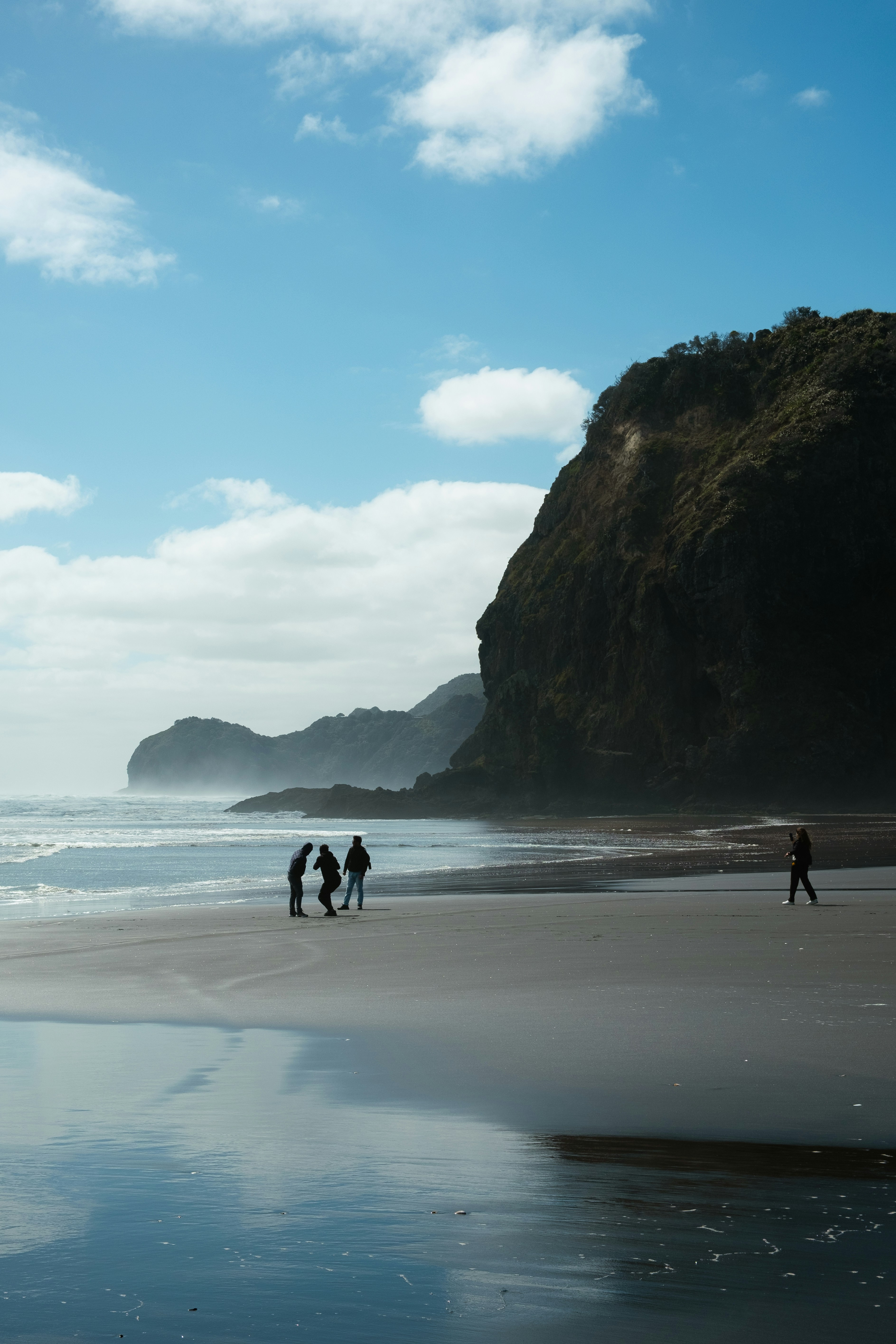 Coastal Silhouette: Figures at the Base of a Sunlit Cliff