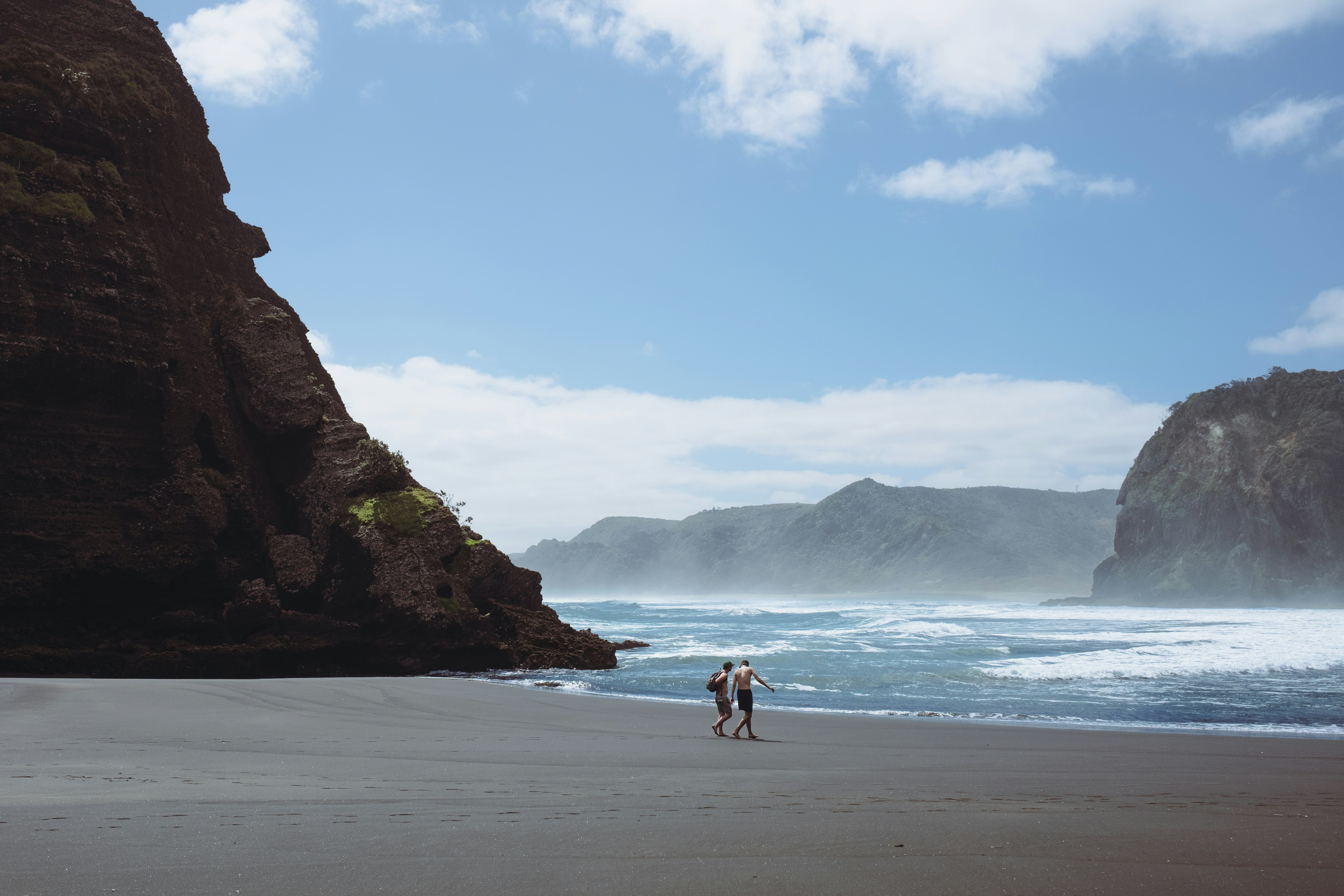 Two hikers at the mouth of a canyoned beach framed by offshore cliffs