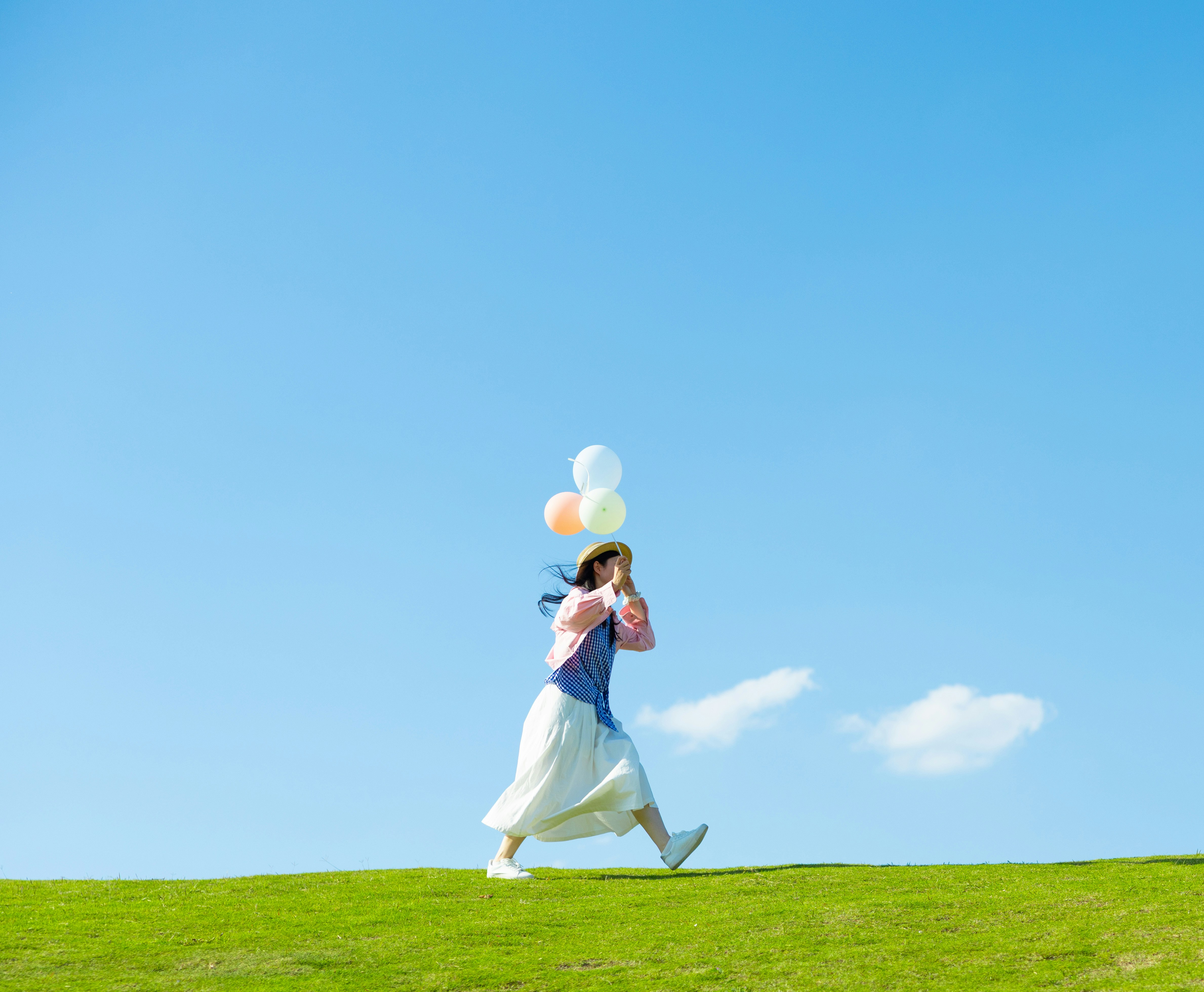 Ballooned Bloom: A girl in a pale dress dances across a grassy crest