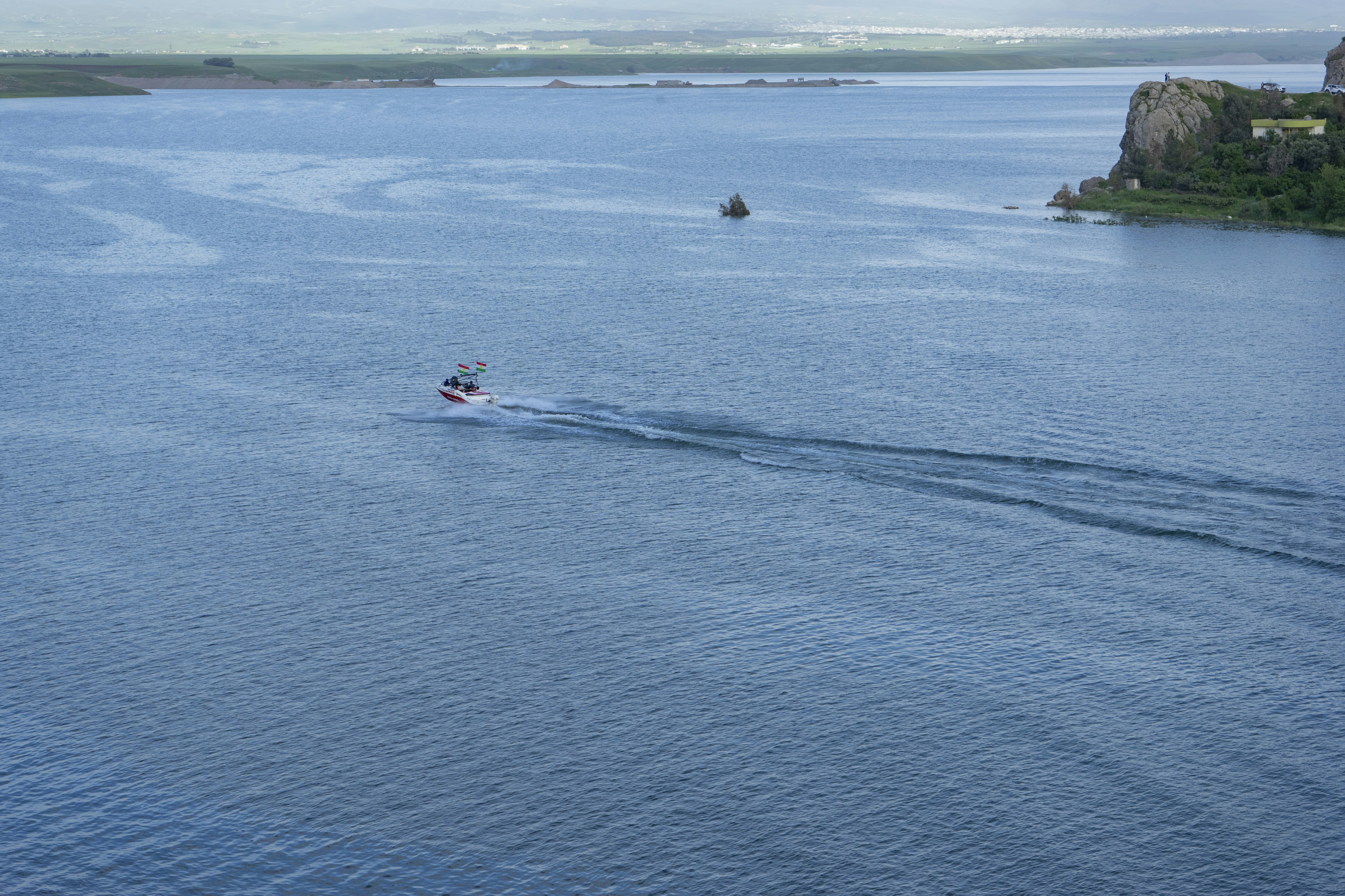 Boat carving a wake through blue expanse past rugged headland