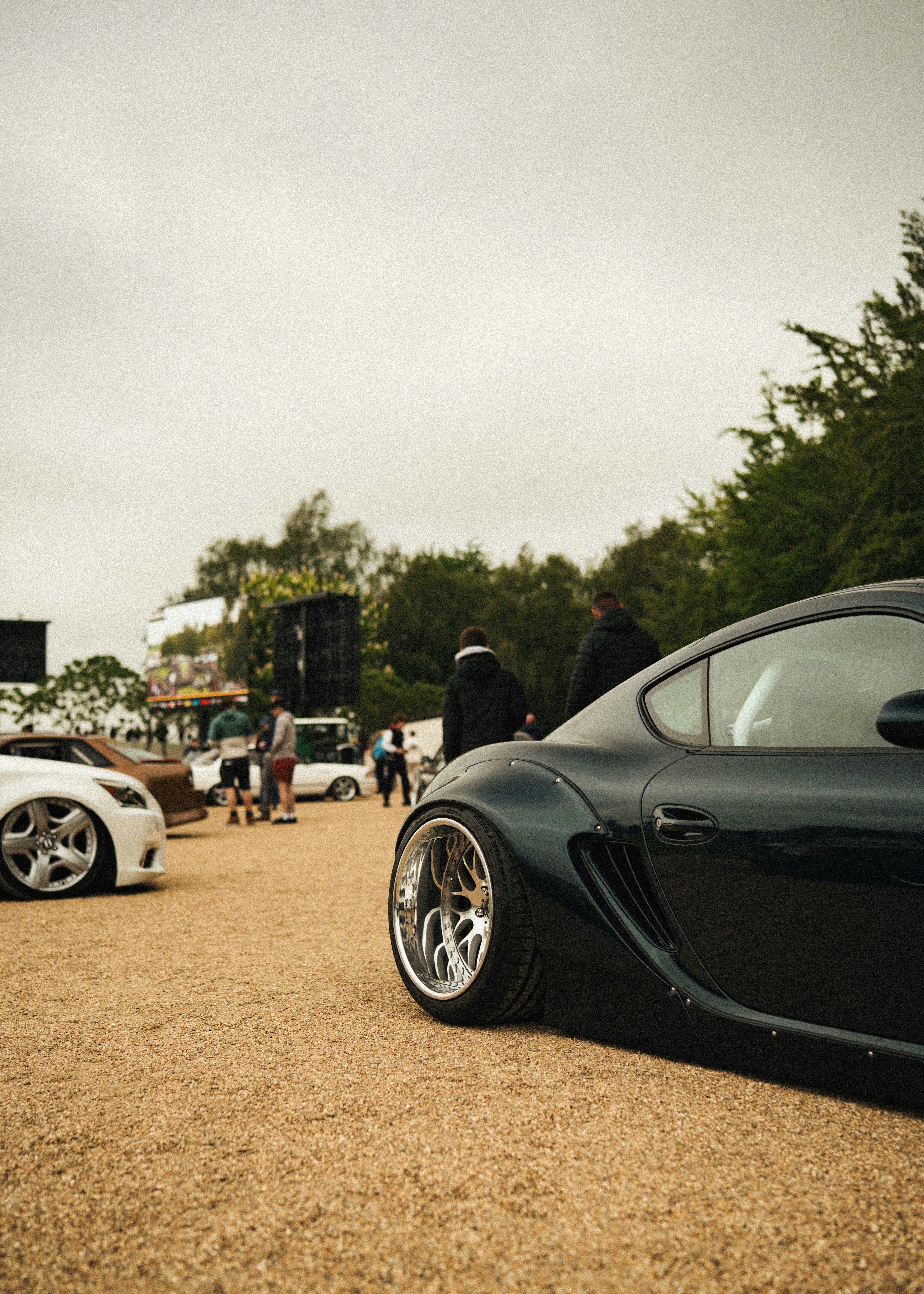 Low-slung Porsches at dusk: chrome wheels and gravel texture