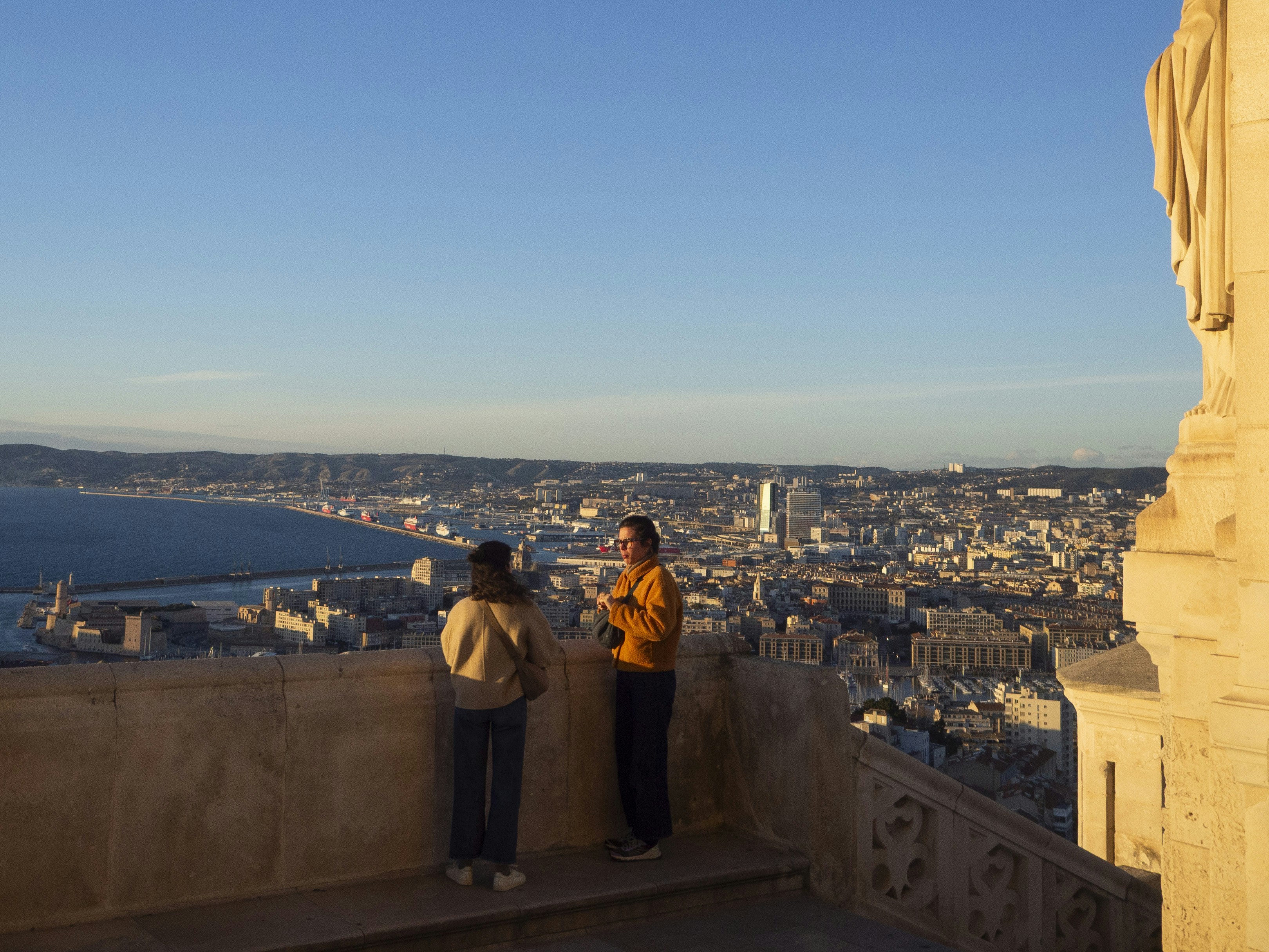 Overlook at the Sunlit Seafront: Two Tourists Conversing by a Historic Terrace