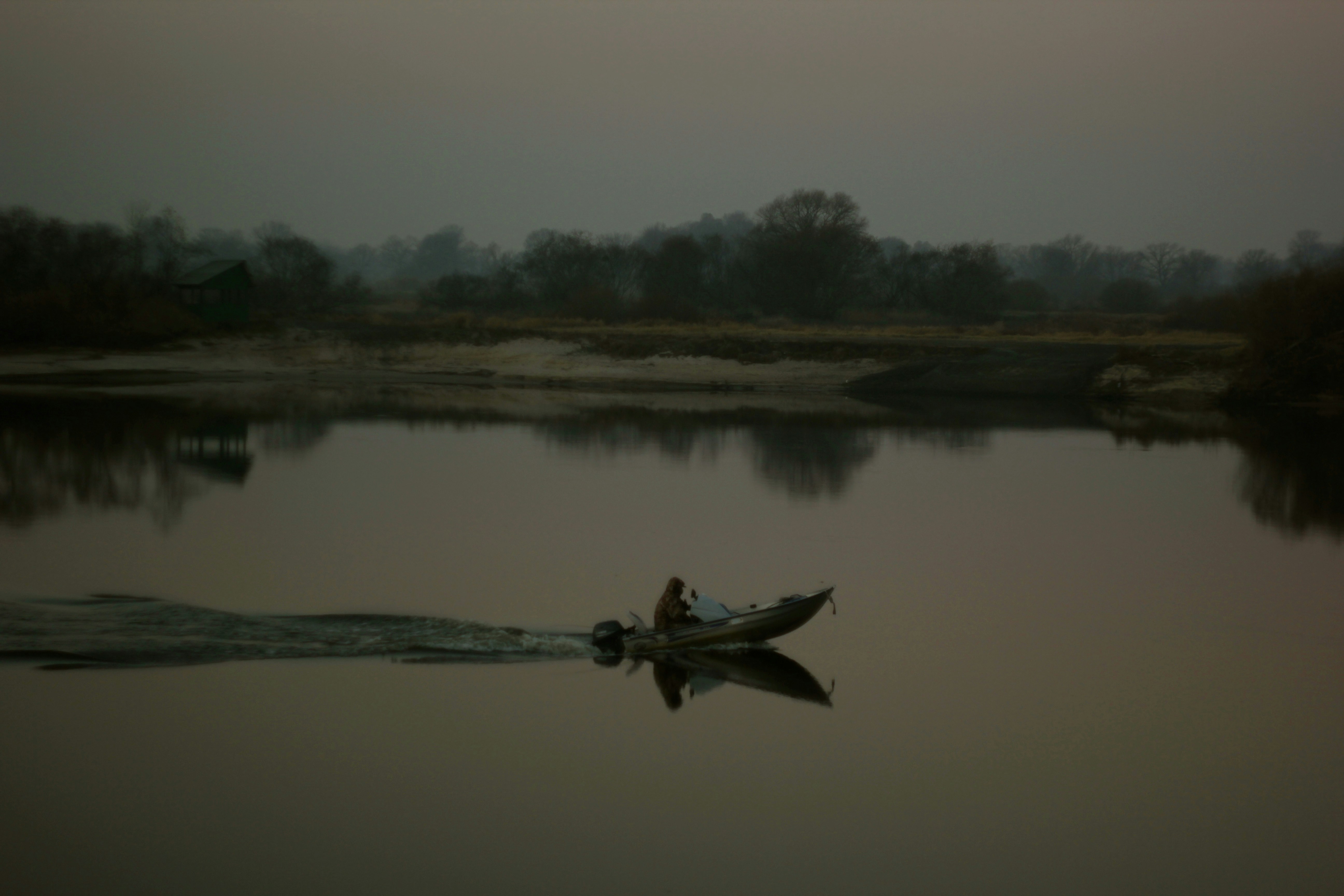 A solitary boat glides across still river at dusk, leaving a soft wake