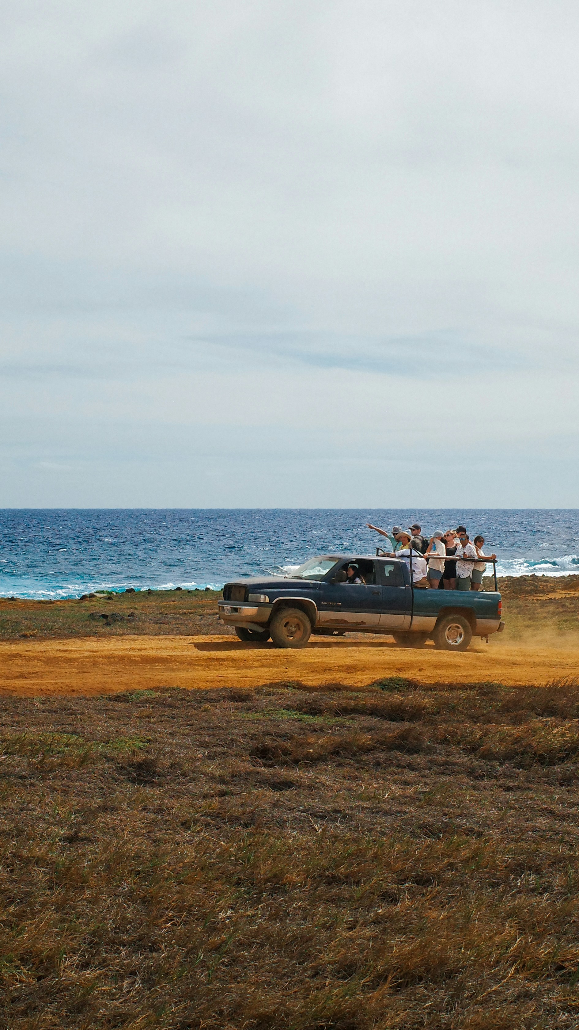 Dusty Joyride: People Lean Out from a Weathered Truck by the Sea