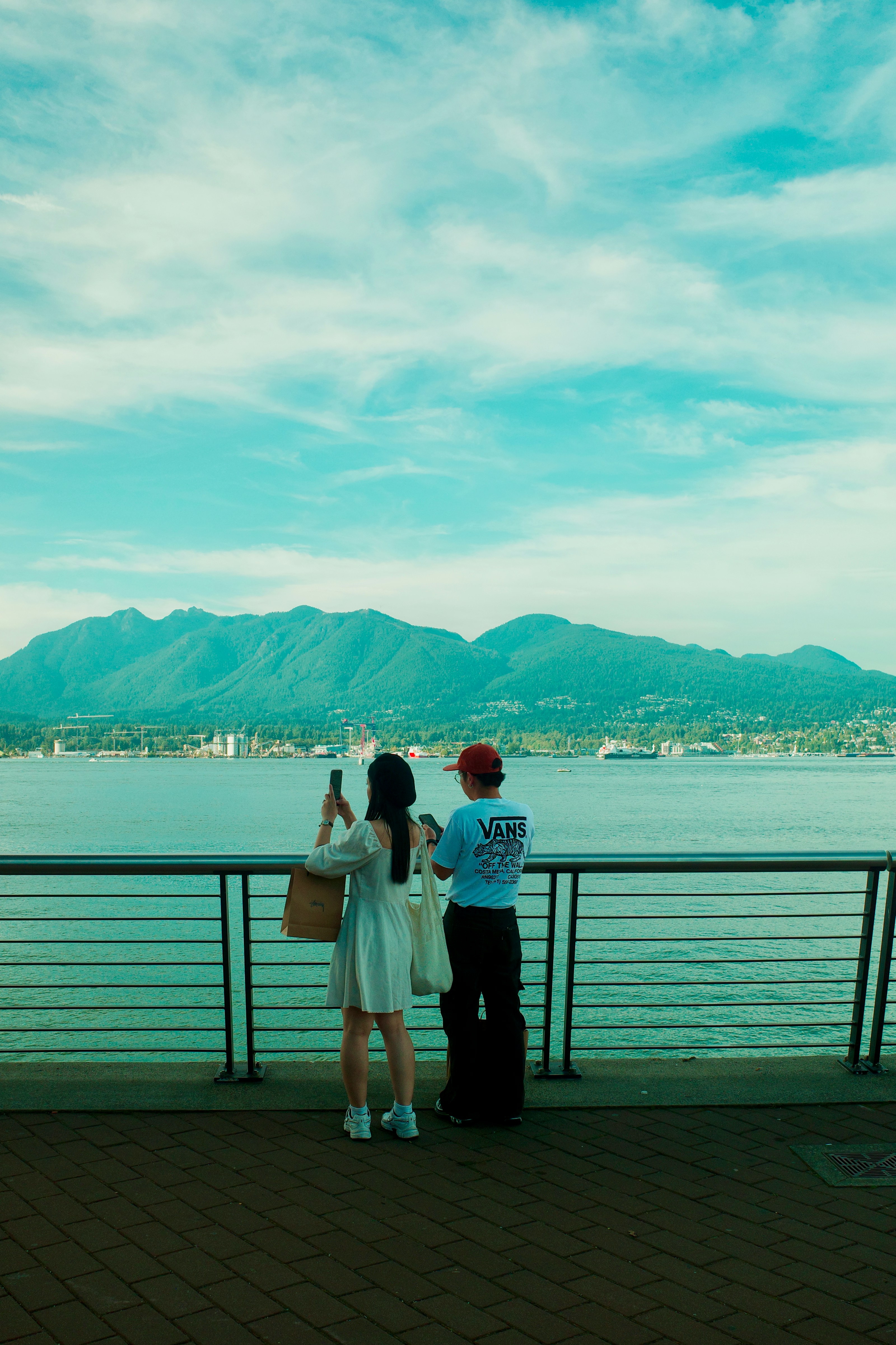 Two Tourists Become the View: A Waterfront Moment by the Distant Mountains