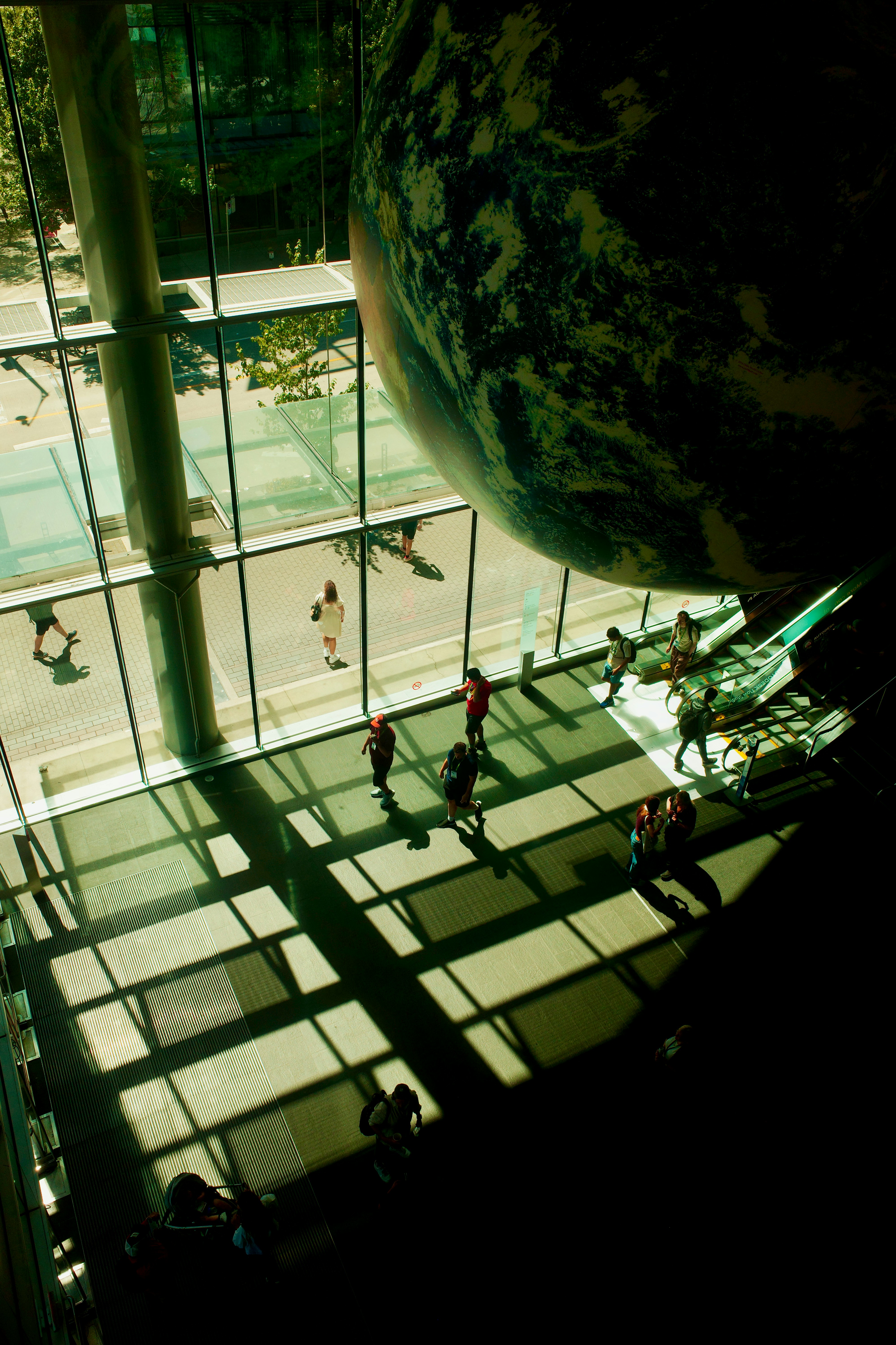 Earthrise Over the Atrium: Aerial View of Shadows and People Beneath a Globe